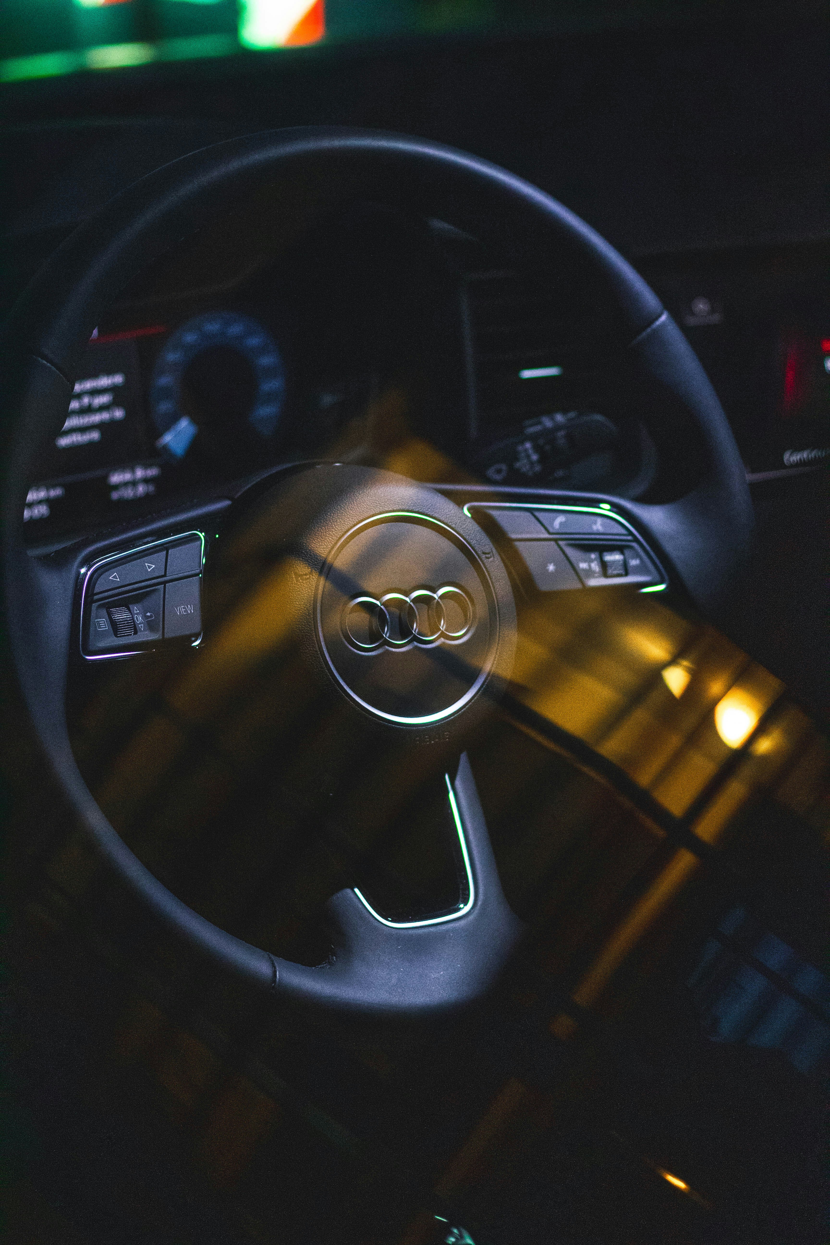 Audi Emblem in Neon Gaze: Close-Up of a Dim Cockpit Steering Wheel