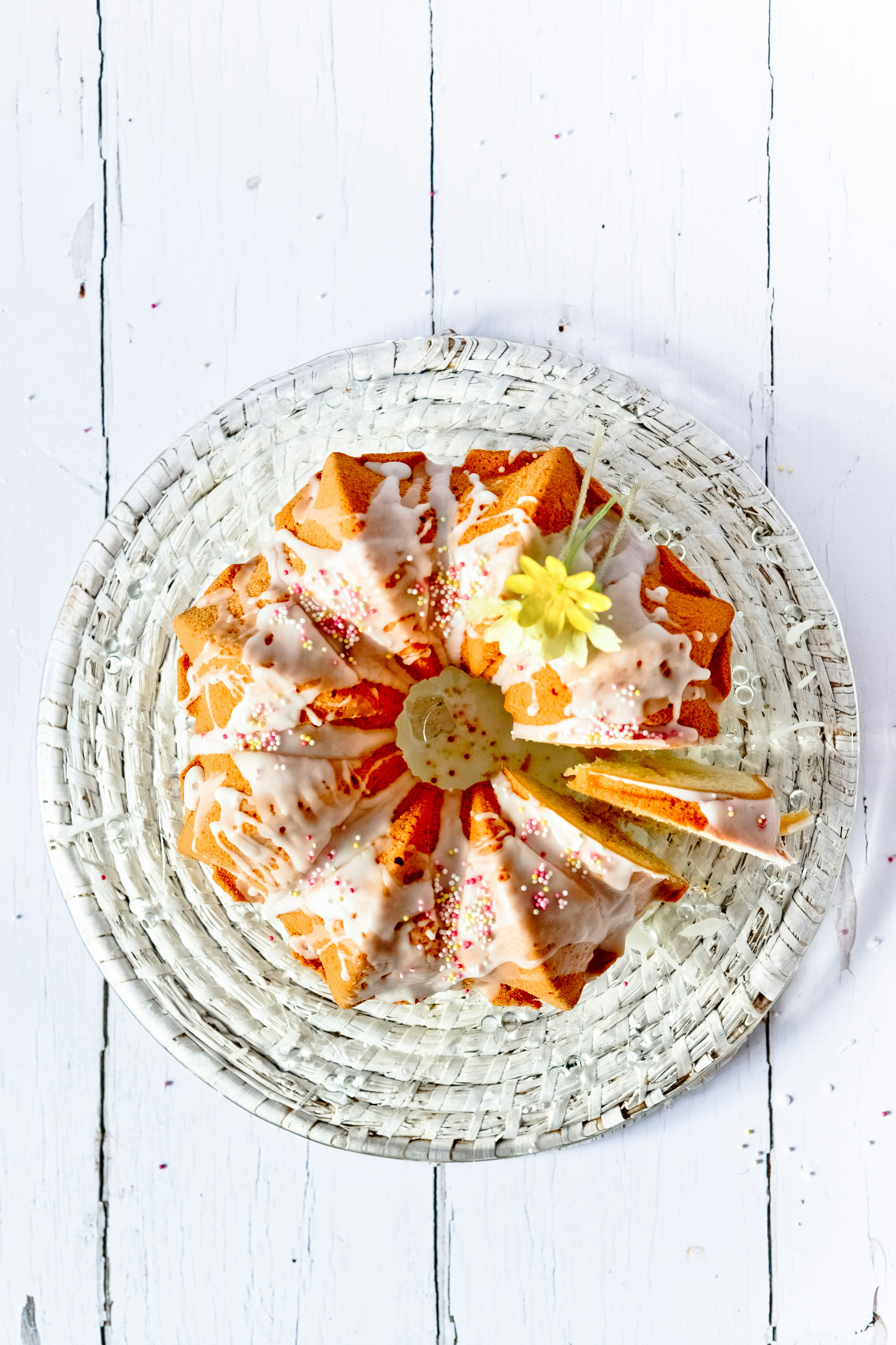 A beautifully decorated bundt cake drizzled with icing, adorned with colorful sprinkles and a vibrant flower at the center.