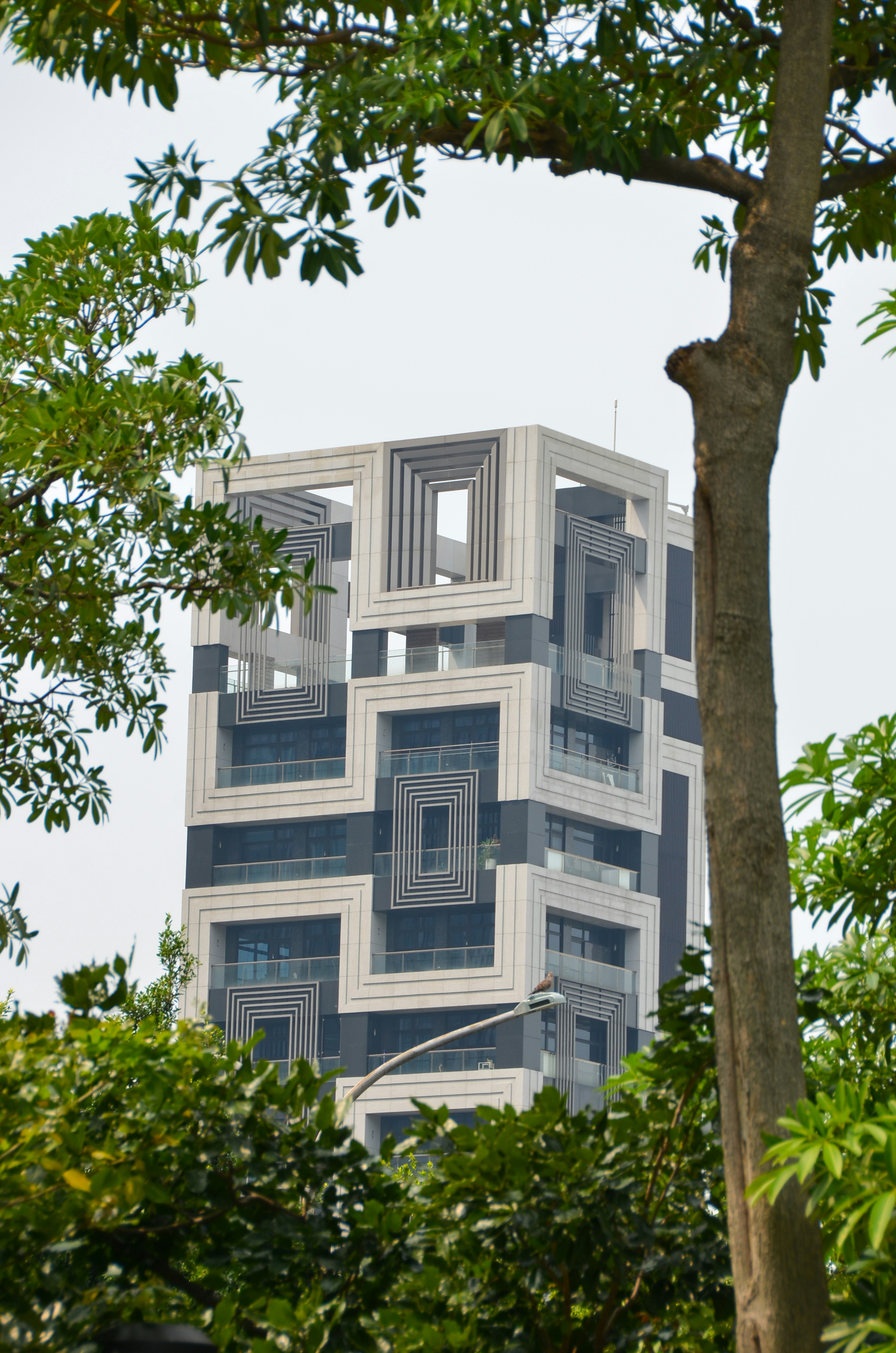Contemporary architectural structure framed by lush greenery, showcasing a unique geometric design. The building's intricate patterns contrast with the surrounding foliage.