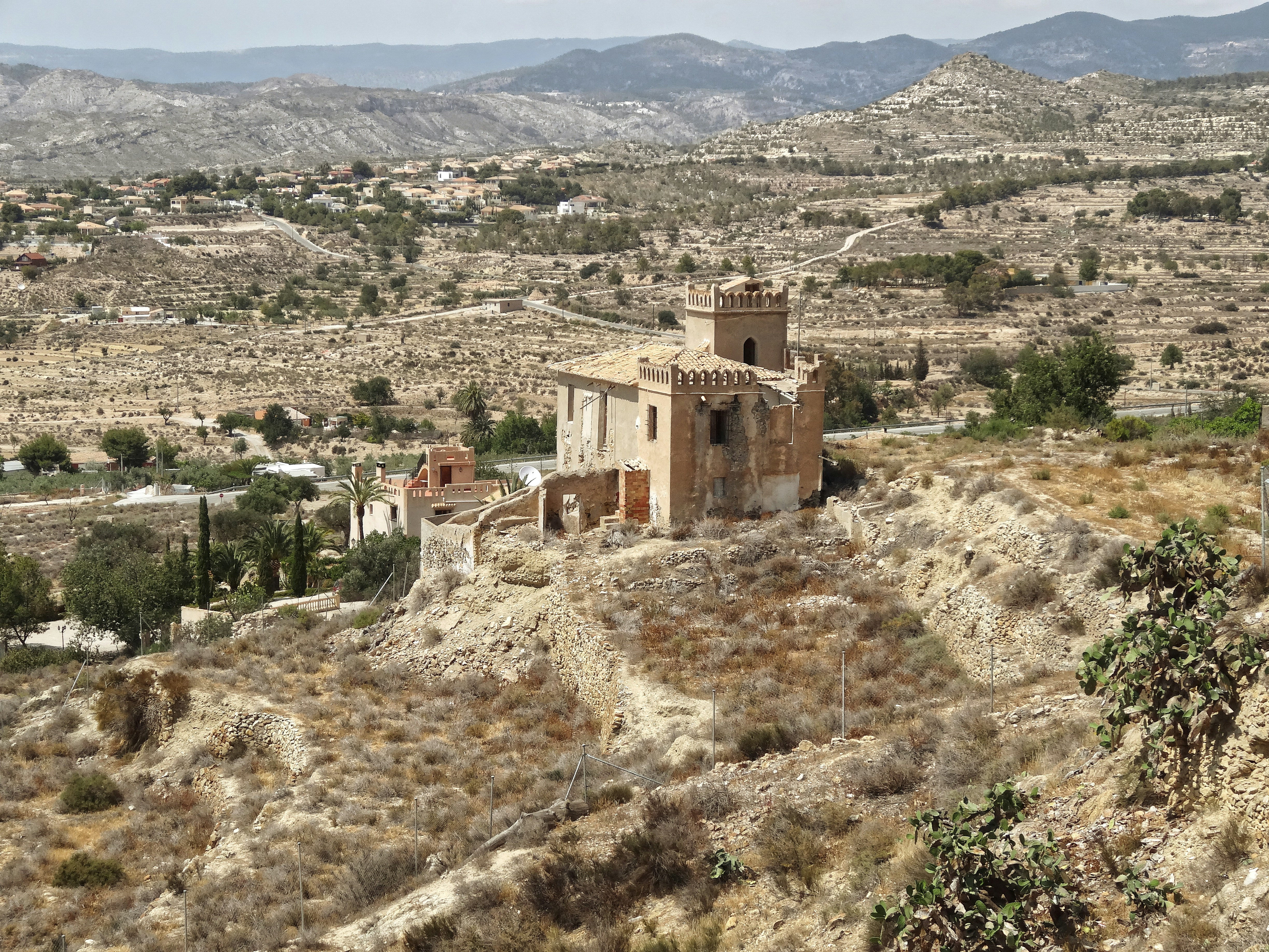 Abandoned stone structure perched on a hillside, surrounded by dry terrain and sparse vegetation.