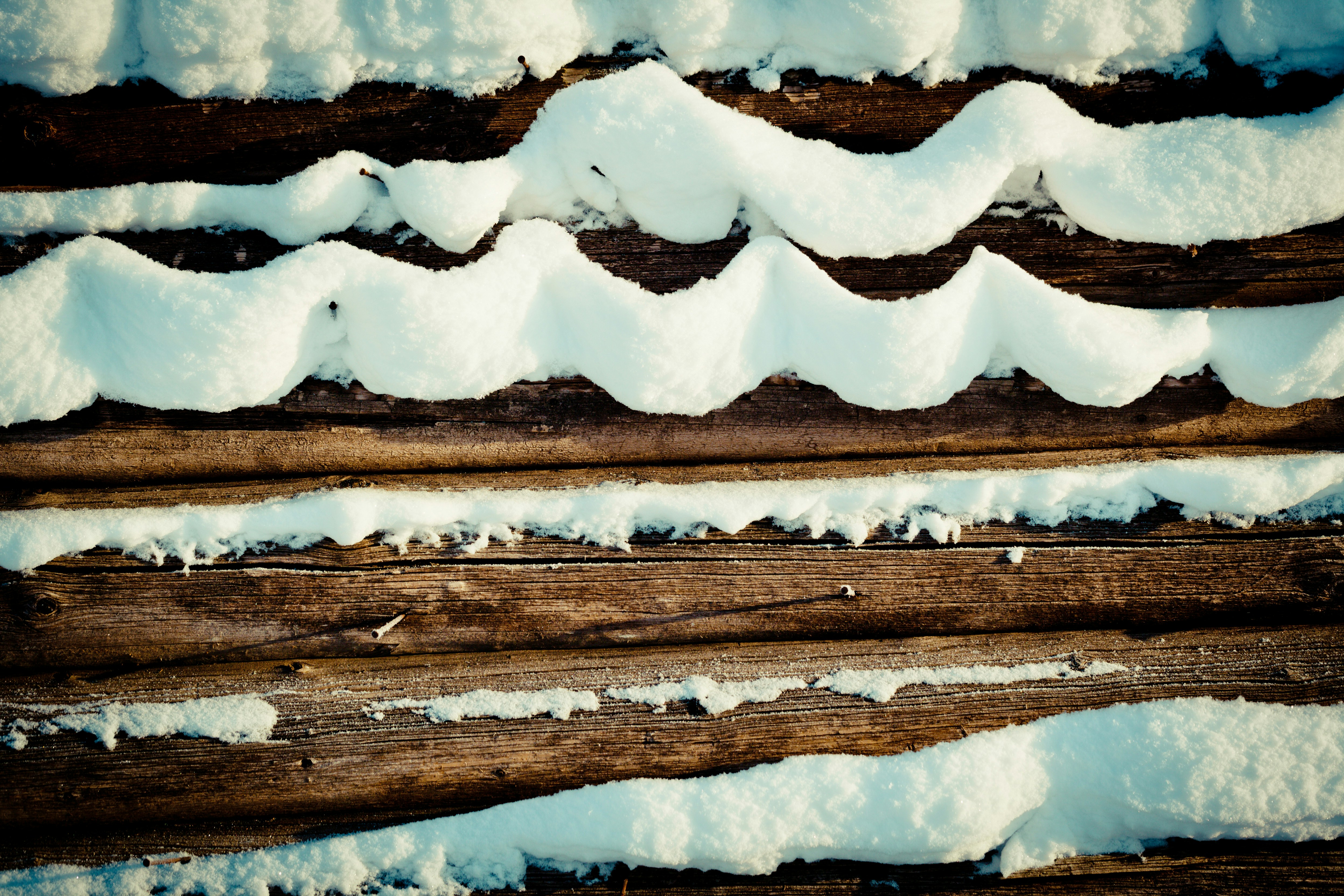 Curved snow drifts resting atop layered wooden logs, showcasing the interplay between nature and texture.
