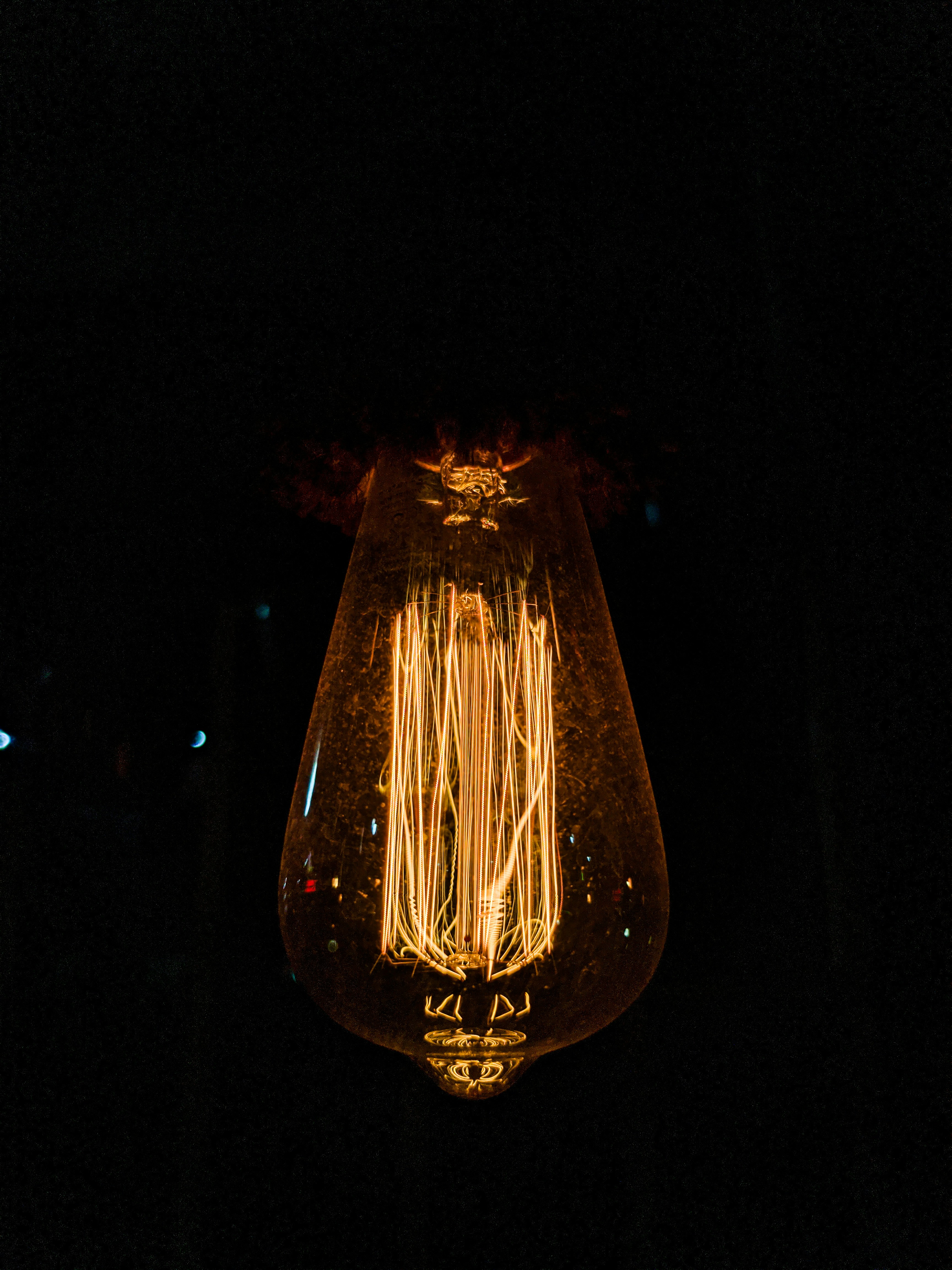 Vintage light bulb glowing against a dark backdrop, showcasing intricate filament patterns. The warm light creates a contrast with the surrounding darkness.