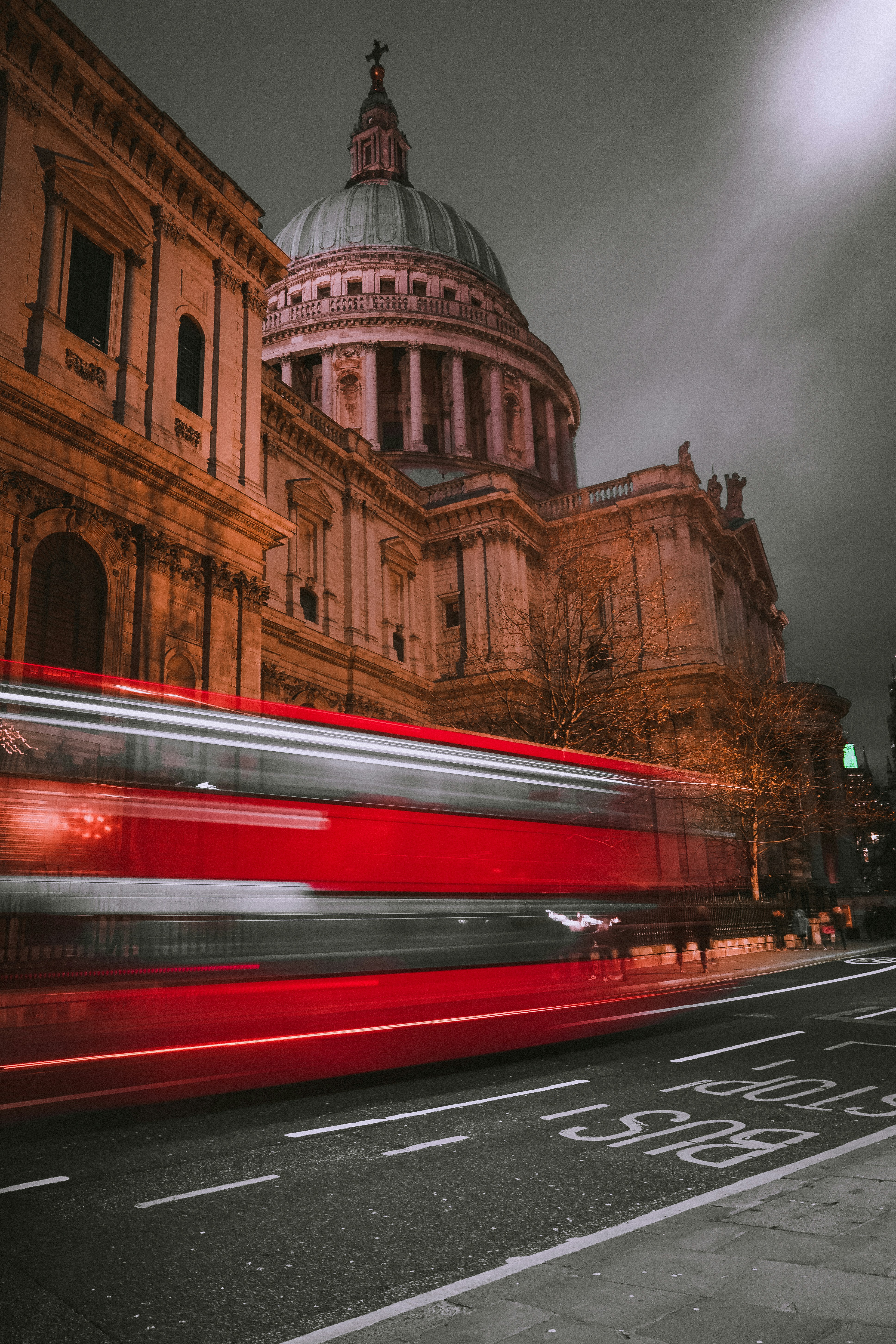 A red double-decker bus blurs past St. Paul's Cathedral, showcasing the vibrant energy of London at dusk.