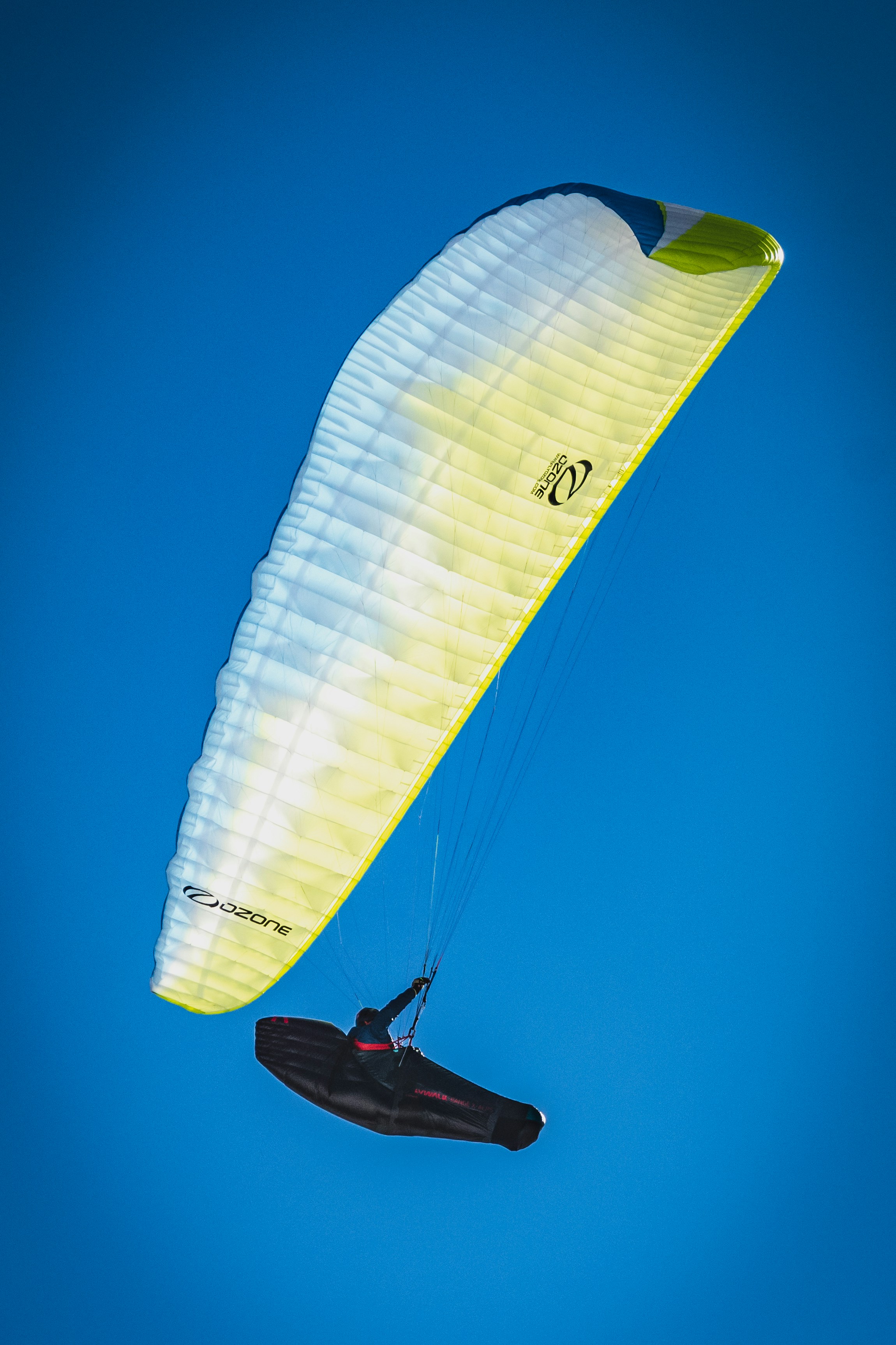 A paraglider gracefully navigates the clear blue sky, showcasing the vibrant colors of the wing. The scene captures the essence of freedom and adventure.