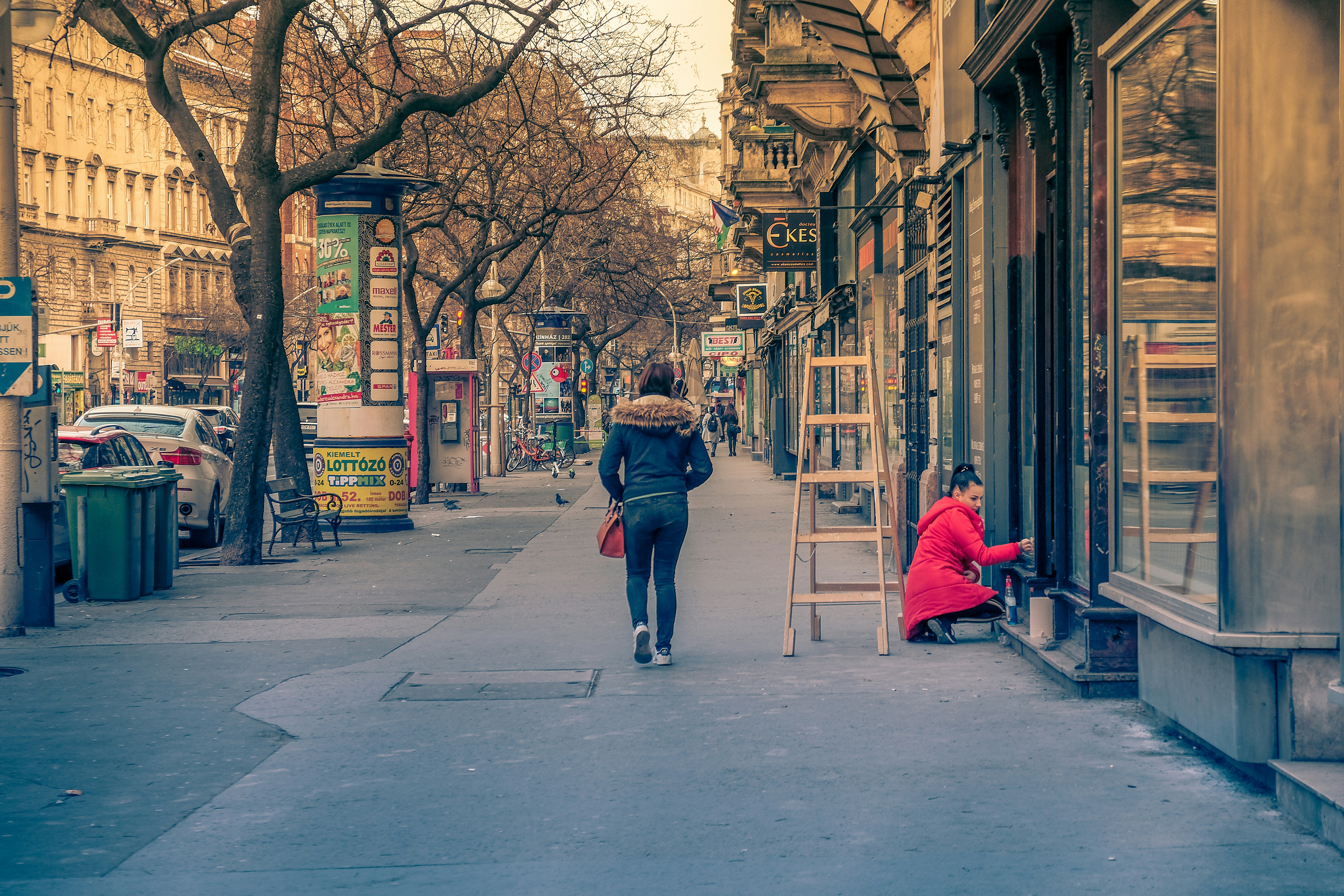 Blue-Tinted Street Silence: A Lone Pedestrian Walks Past a Red-Jacket Figure