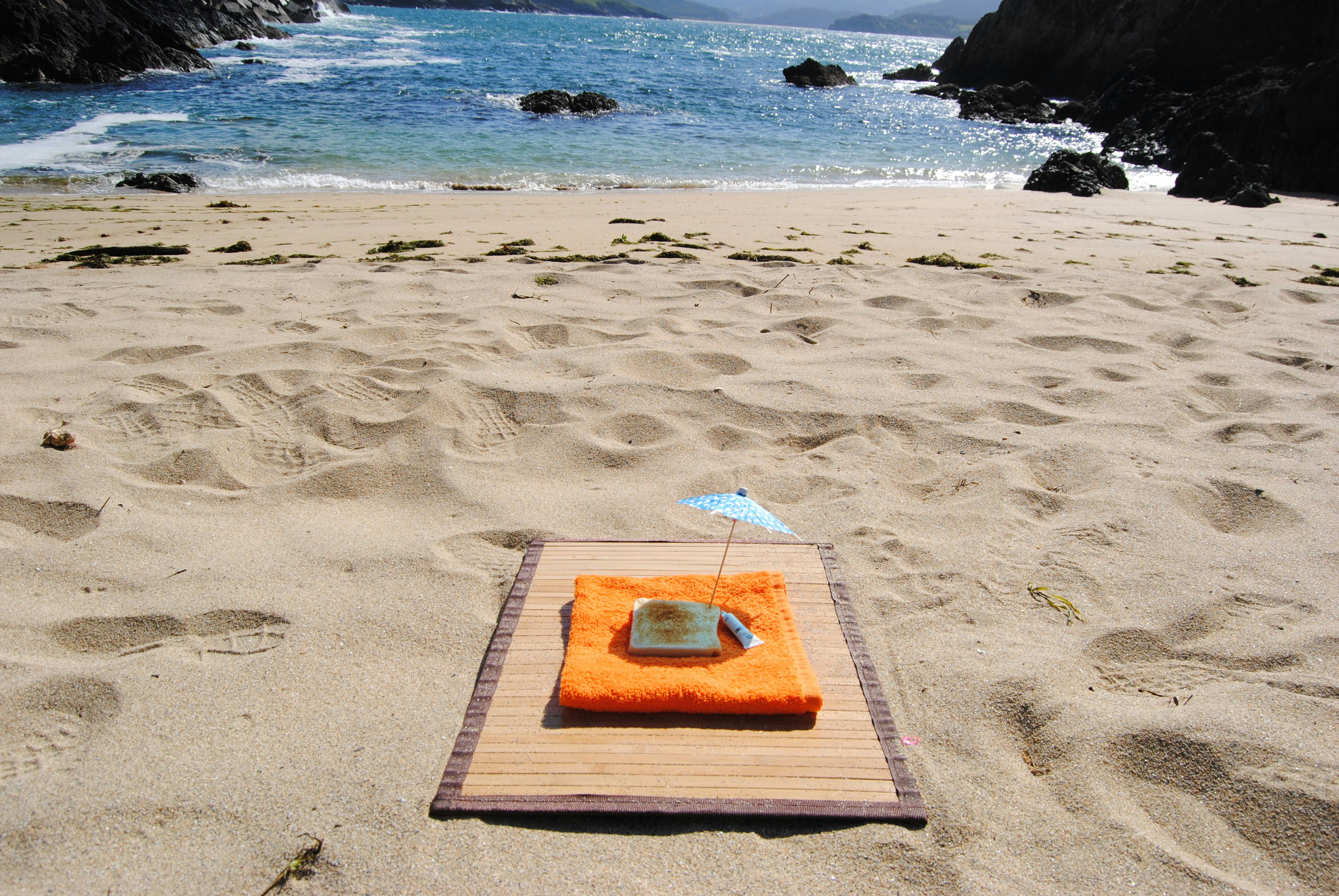 Beach Mat with Orange Pillow and Mini Umbrella Resting by the Ocean