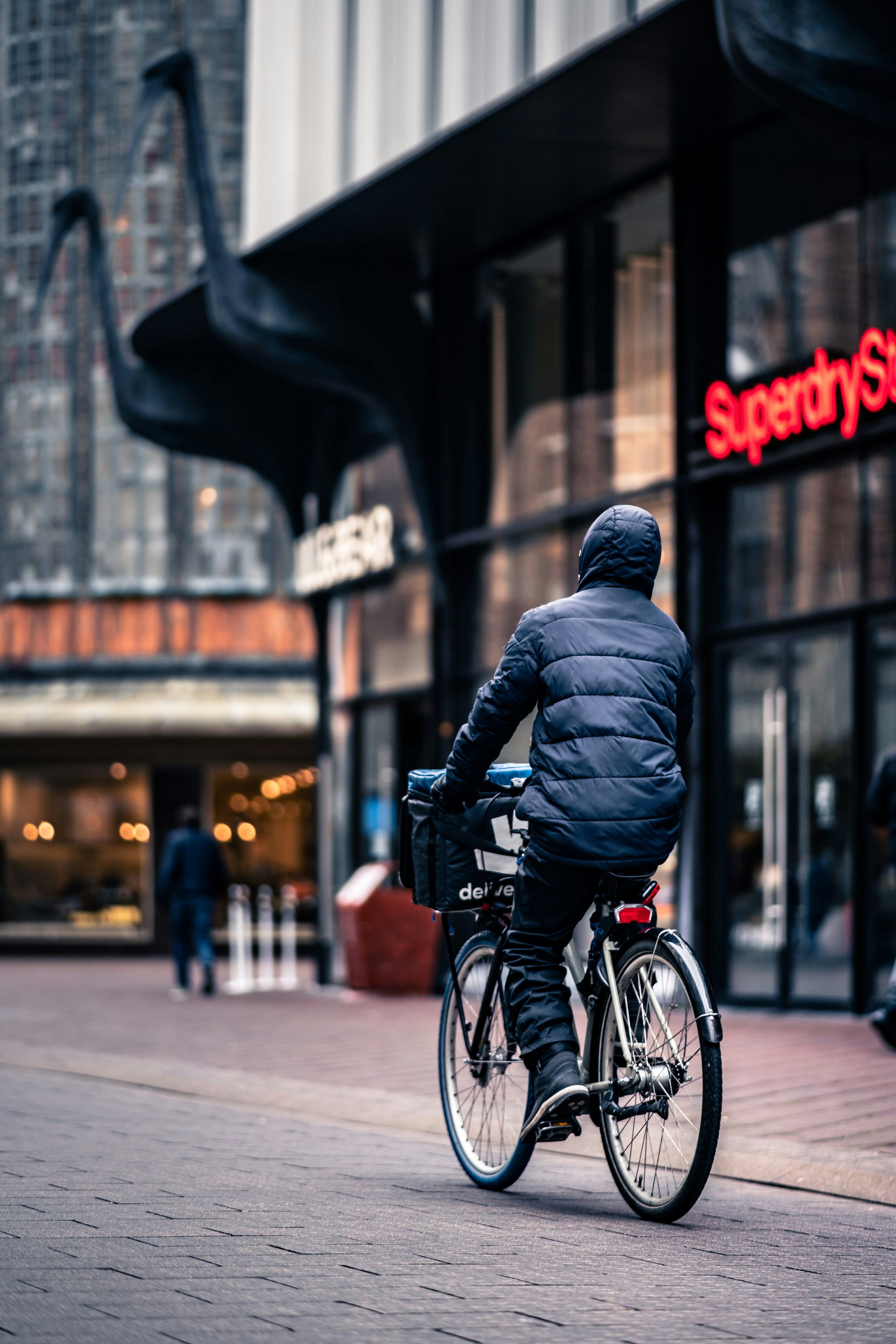 Cyclist on a bicycle navigating through a modern urban environment, with storefronts in the background.