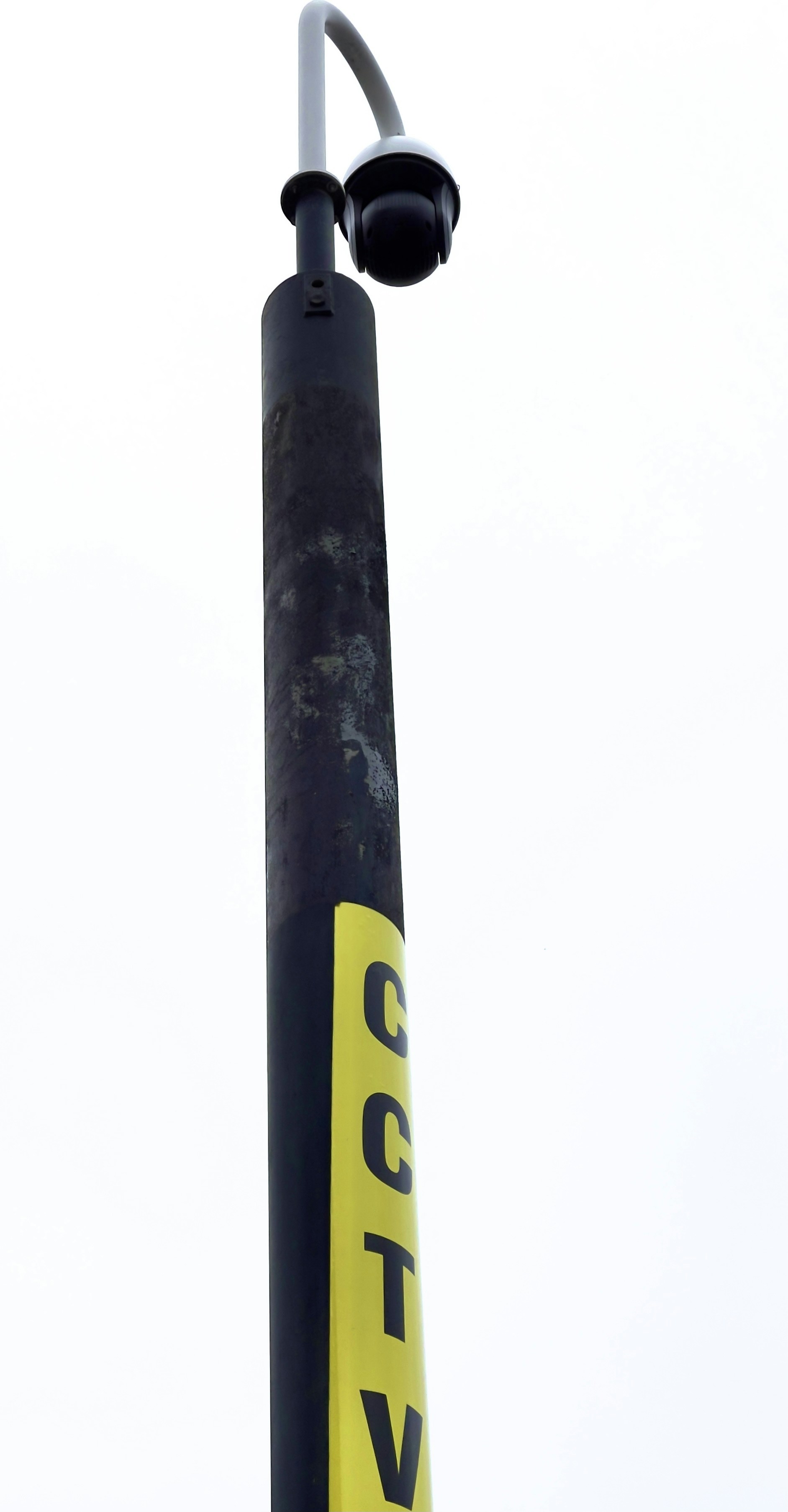 CCTV camera mounted on a tall pole, prominently displaying a yellow 'CCTV' label against a gray sky.