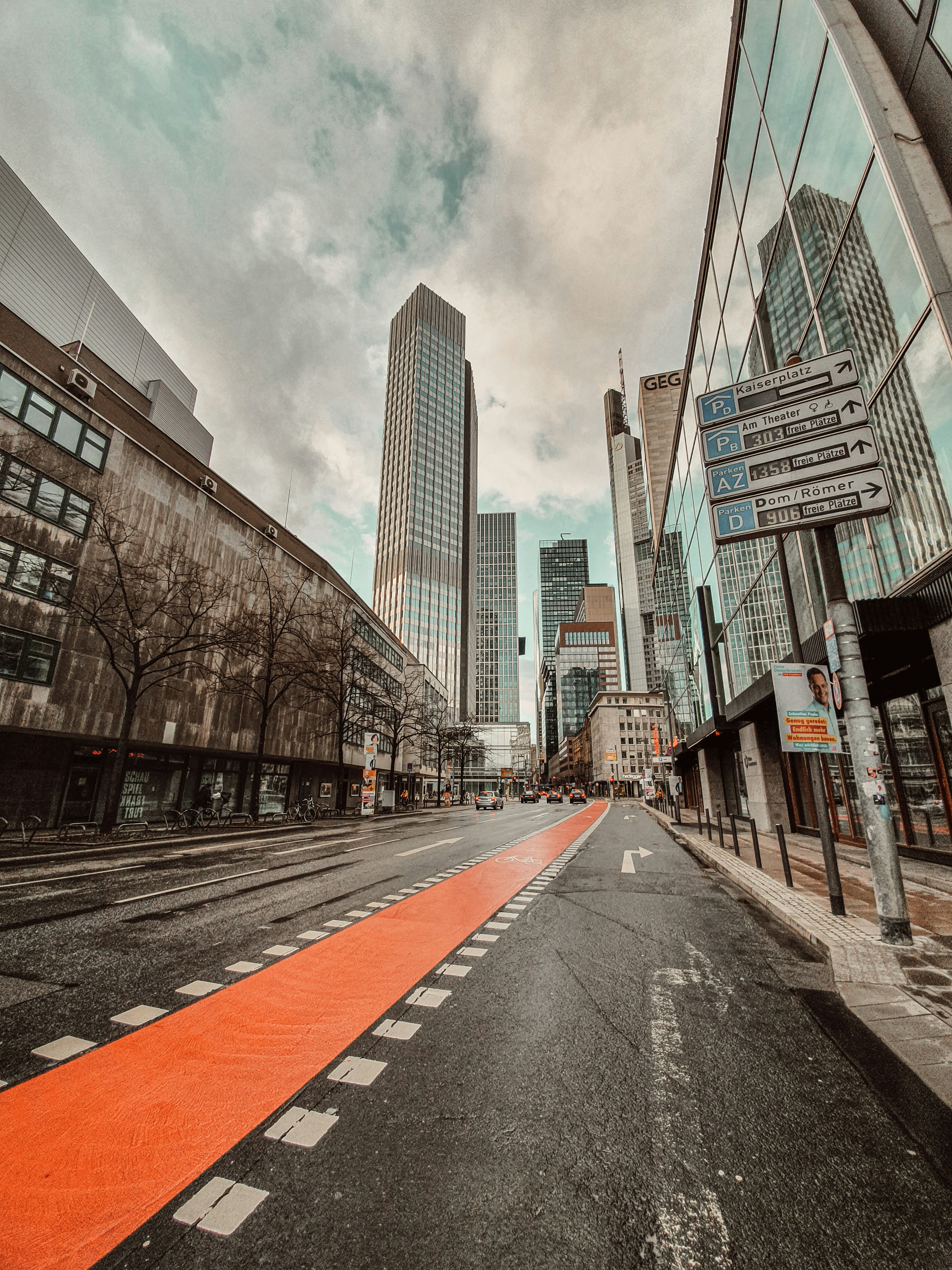 gray concrete road between high rise buildings under white clouds during daytime