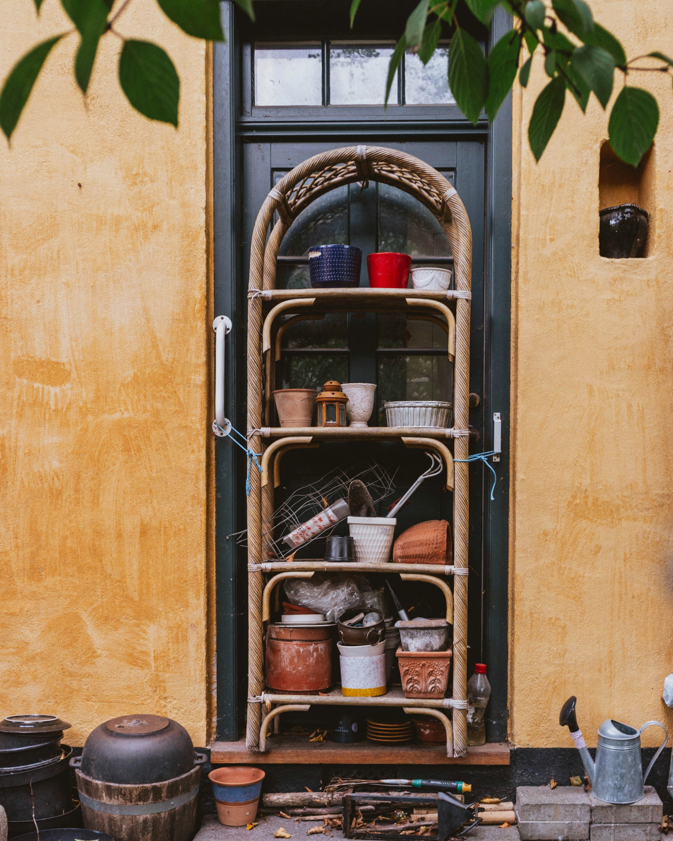 A rustic shelving unit filled with an assortment of colorful pots and gardening tools against a warm yellow wall. The arrangement showcases a blend of textures and colors.