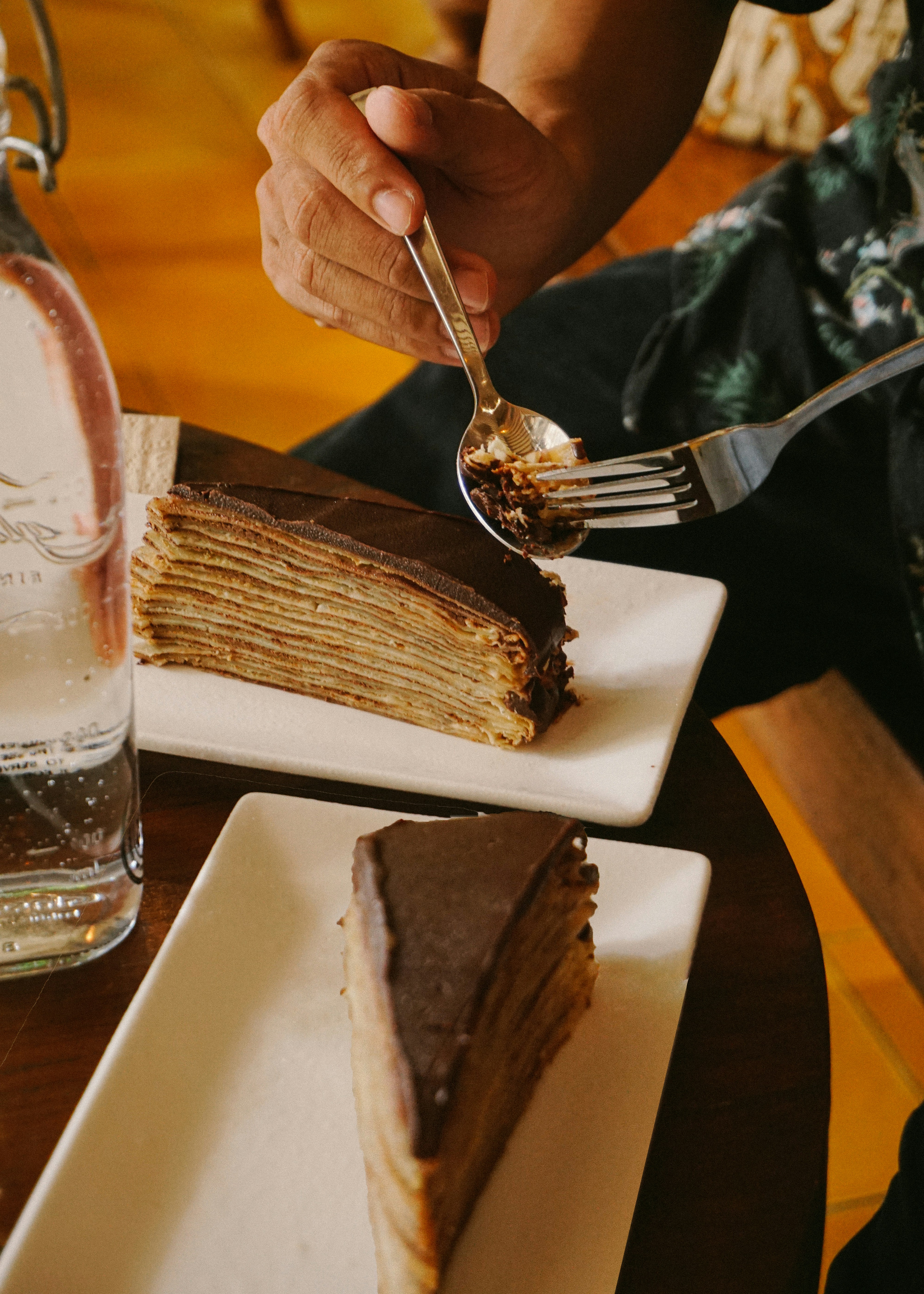 Layered Chocolate Slice in Warm Focus: Hands, Fork, and Creamy Texture