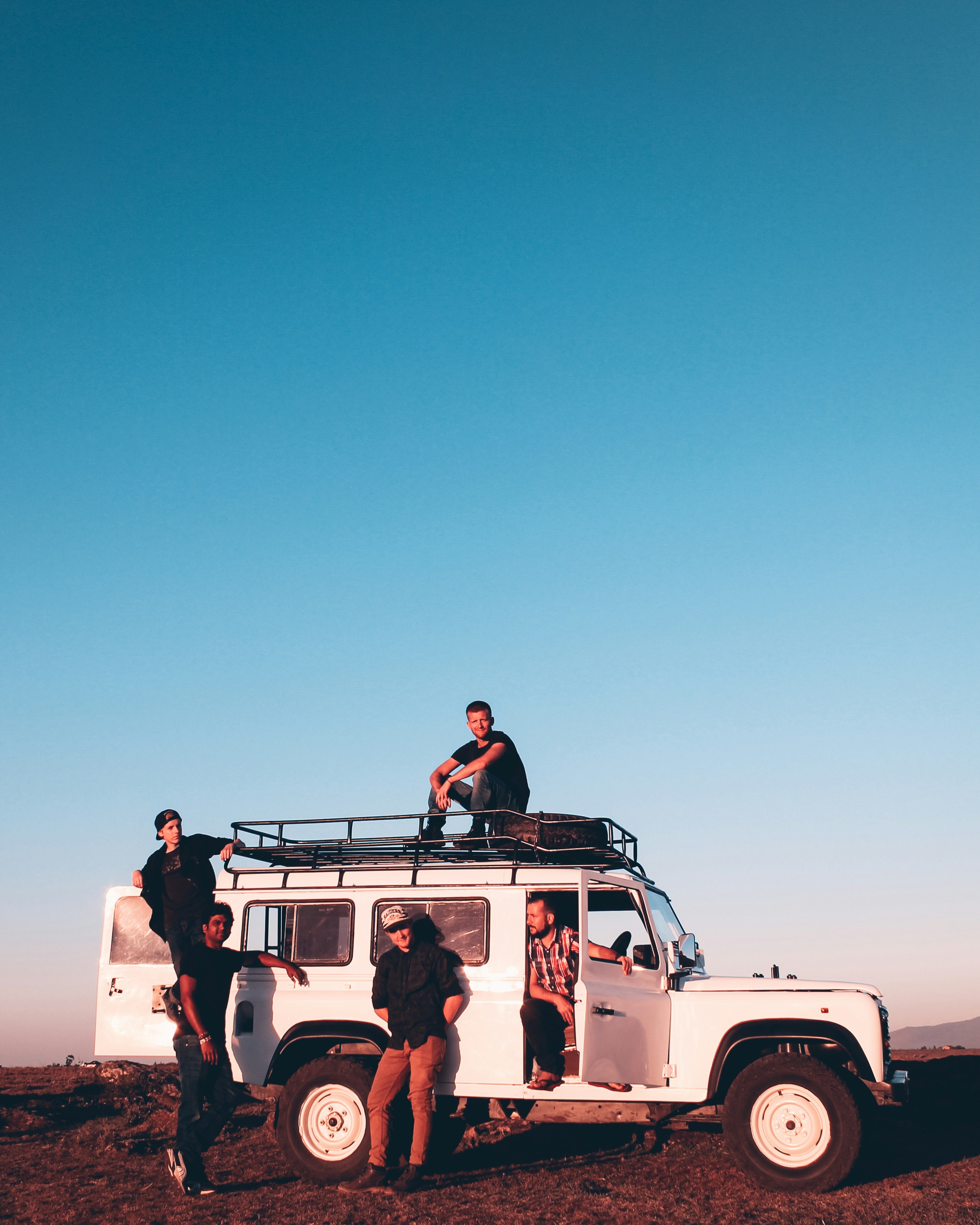 Group of friends posing around a vintage off-road vehicle against a clear blue sky, embodying the spirit of adventure.