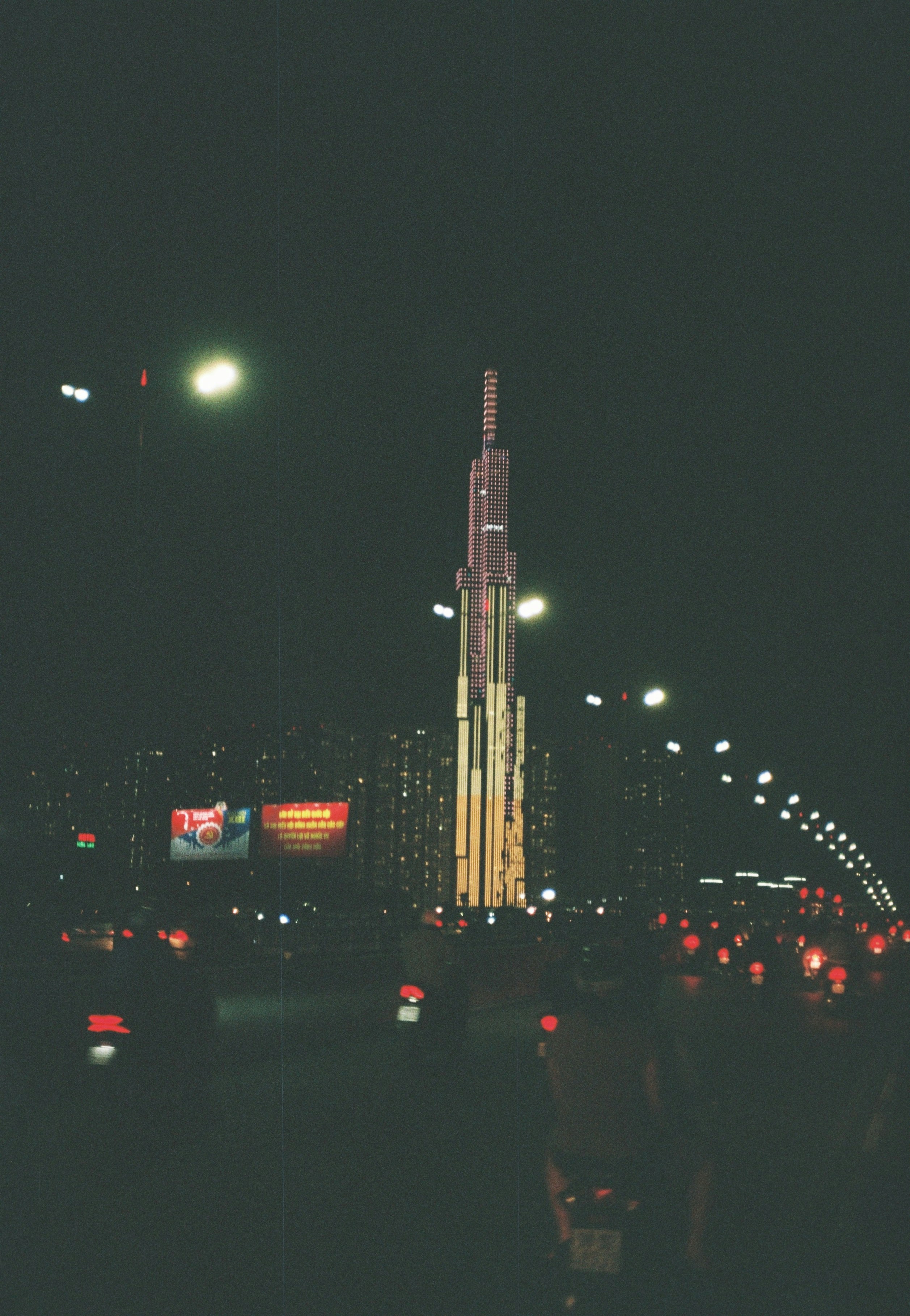 Illuminated skyscraper towers over bustling traffic on a city bridge at night. Neon lights reflect the vibrant energy of urban life.