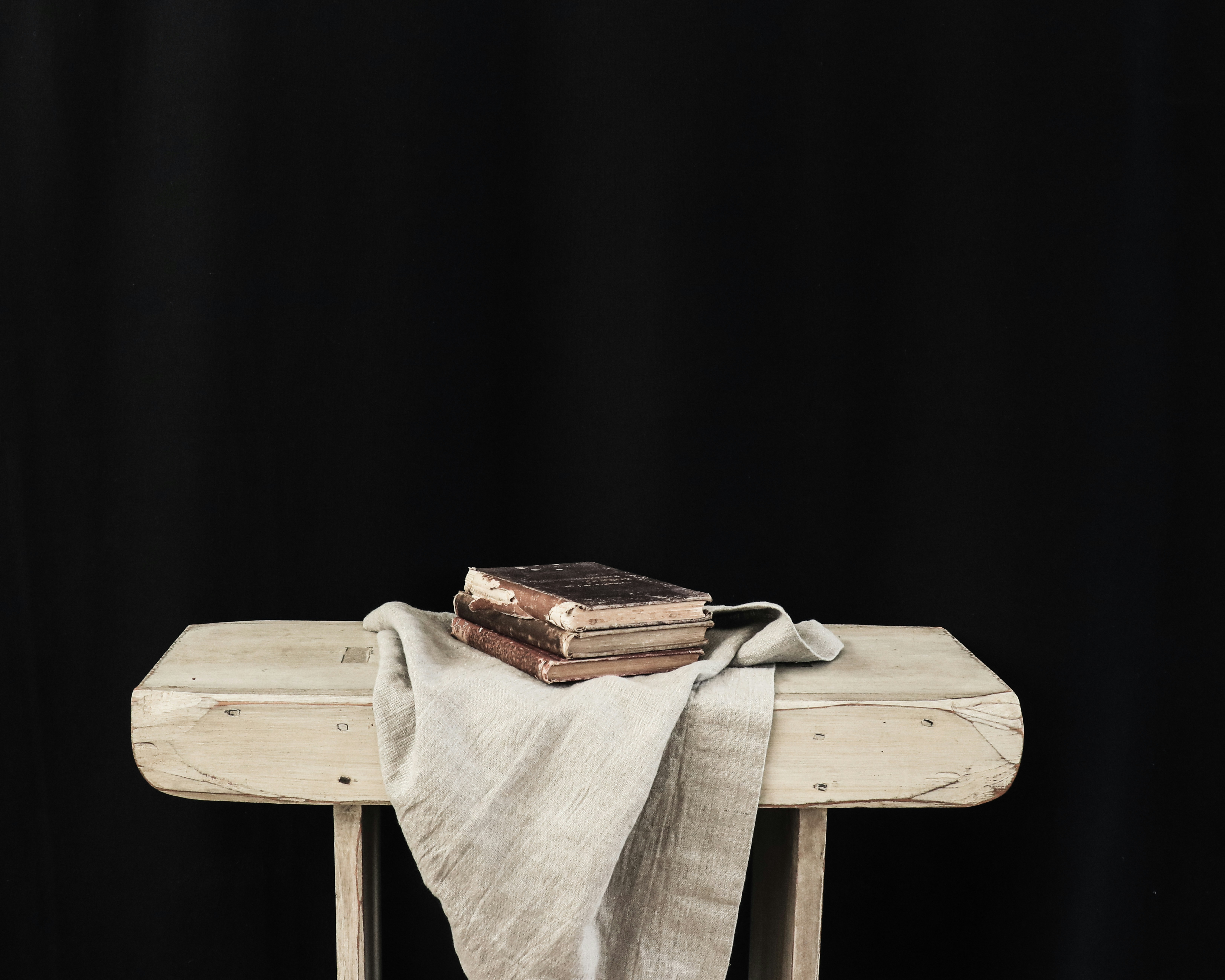 Quiet Library Ritual: Two aged volumes on a weathered stool against a black backdrop
