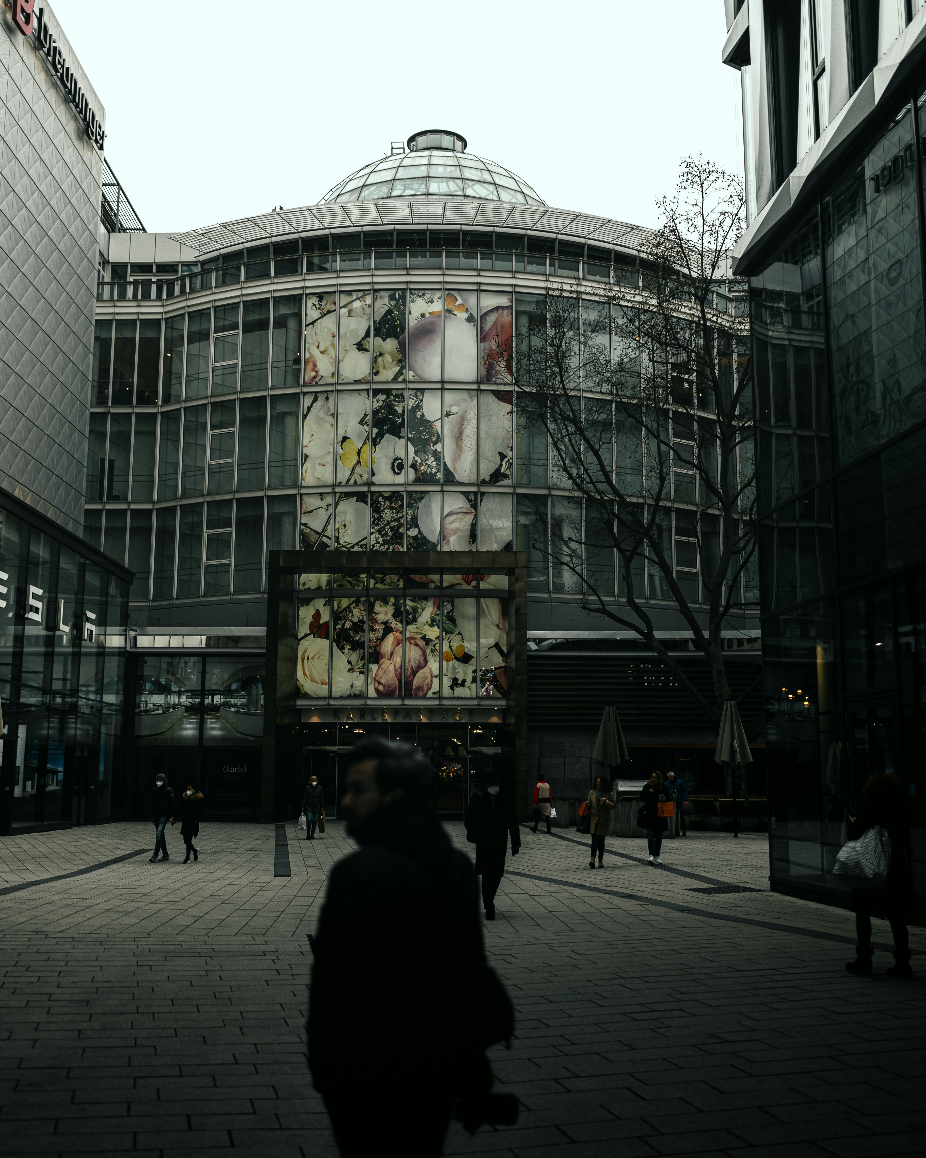 A vibrant advertisement featuring an array of food items decorates the exterior of a modern building, surrounded by pedestrians in an urban setting.
