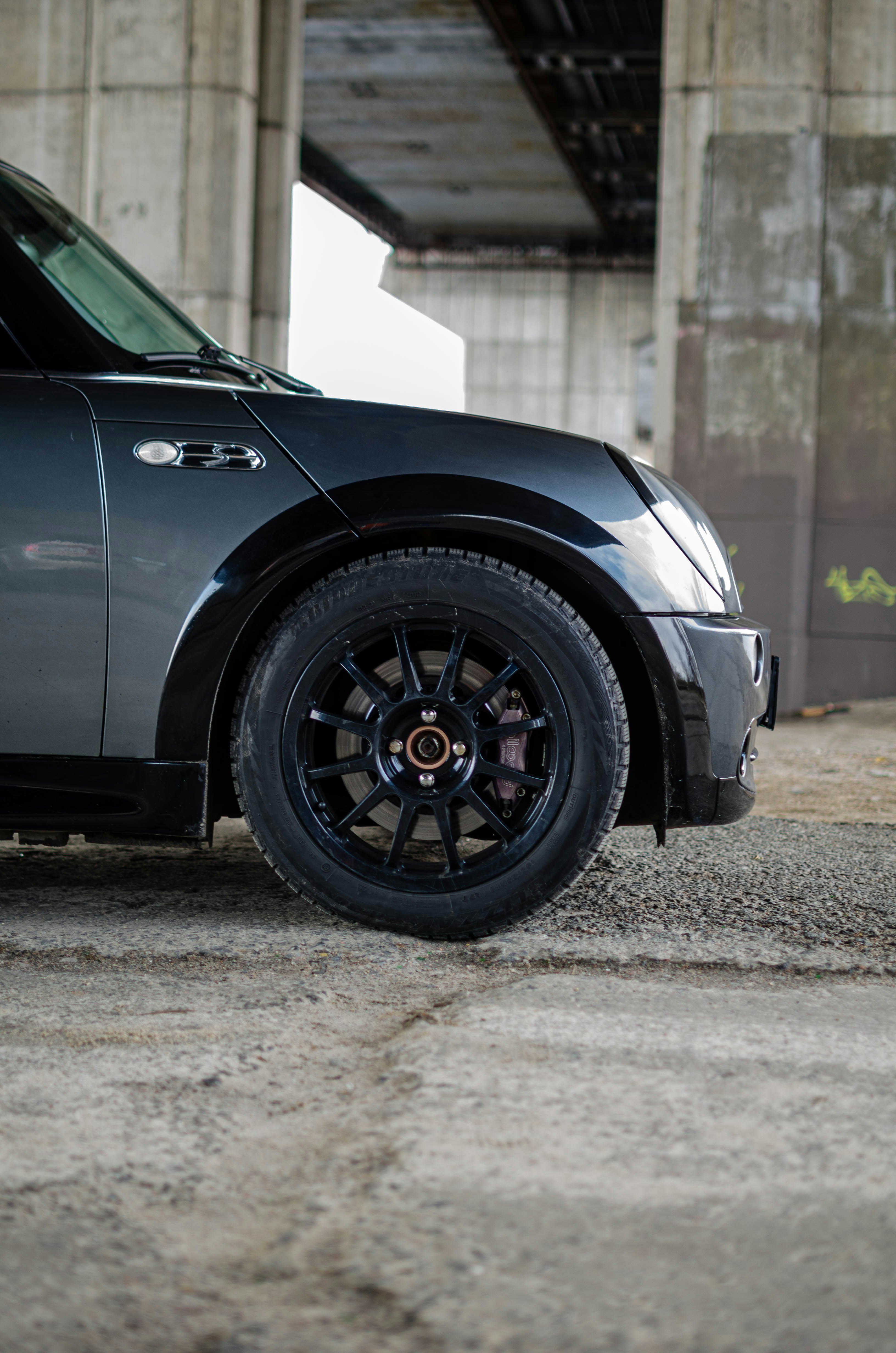 Low-Angle Portrait of a Dark Car Under an Industrial Overpass