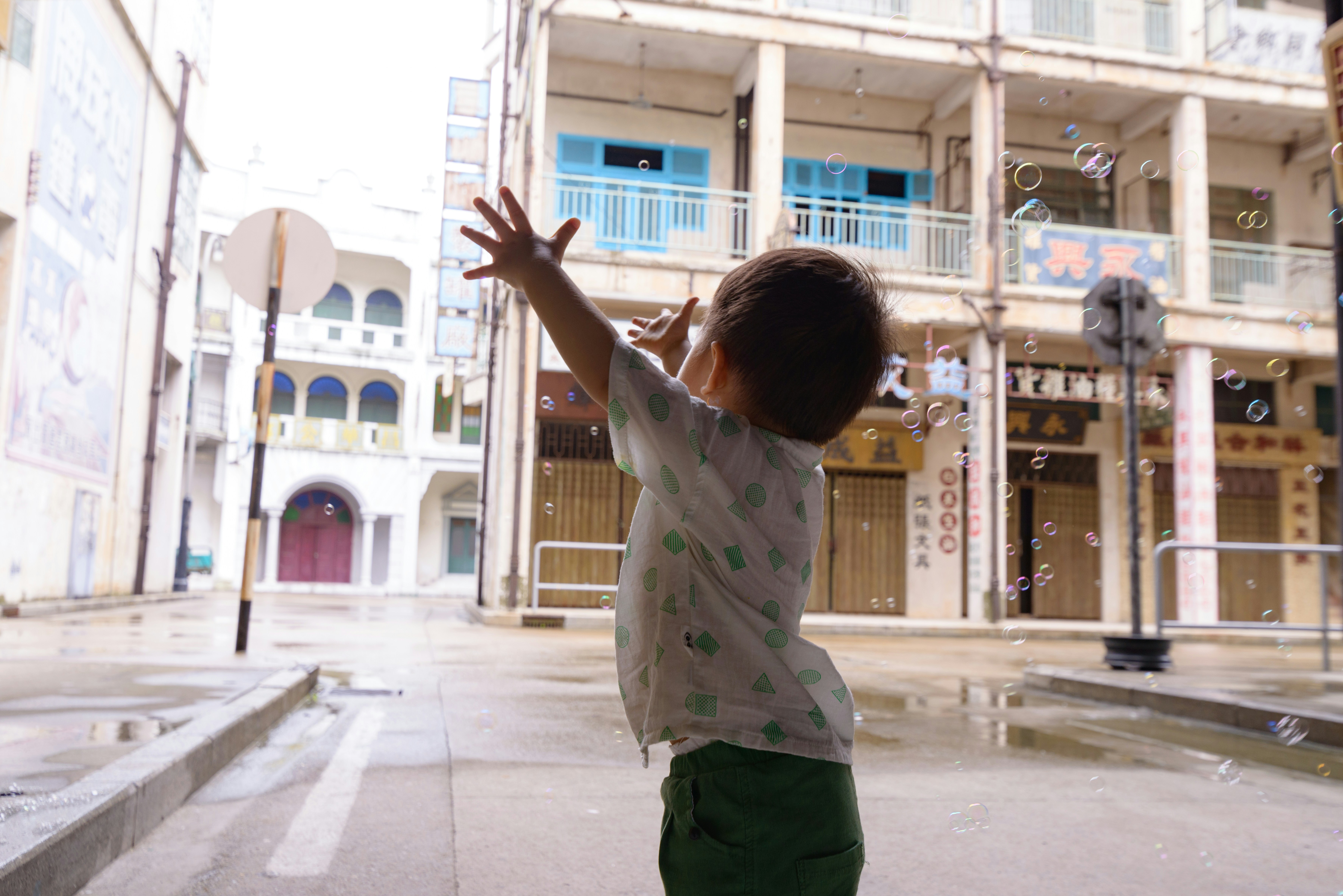 Joyful Reach: A Child Plays Under Floating Bubbles in an Urban Square