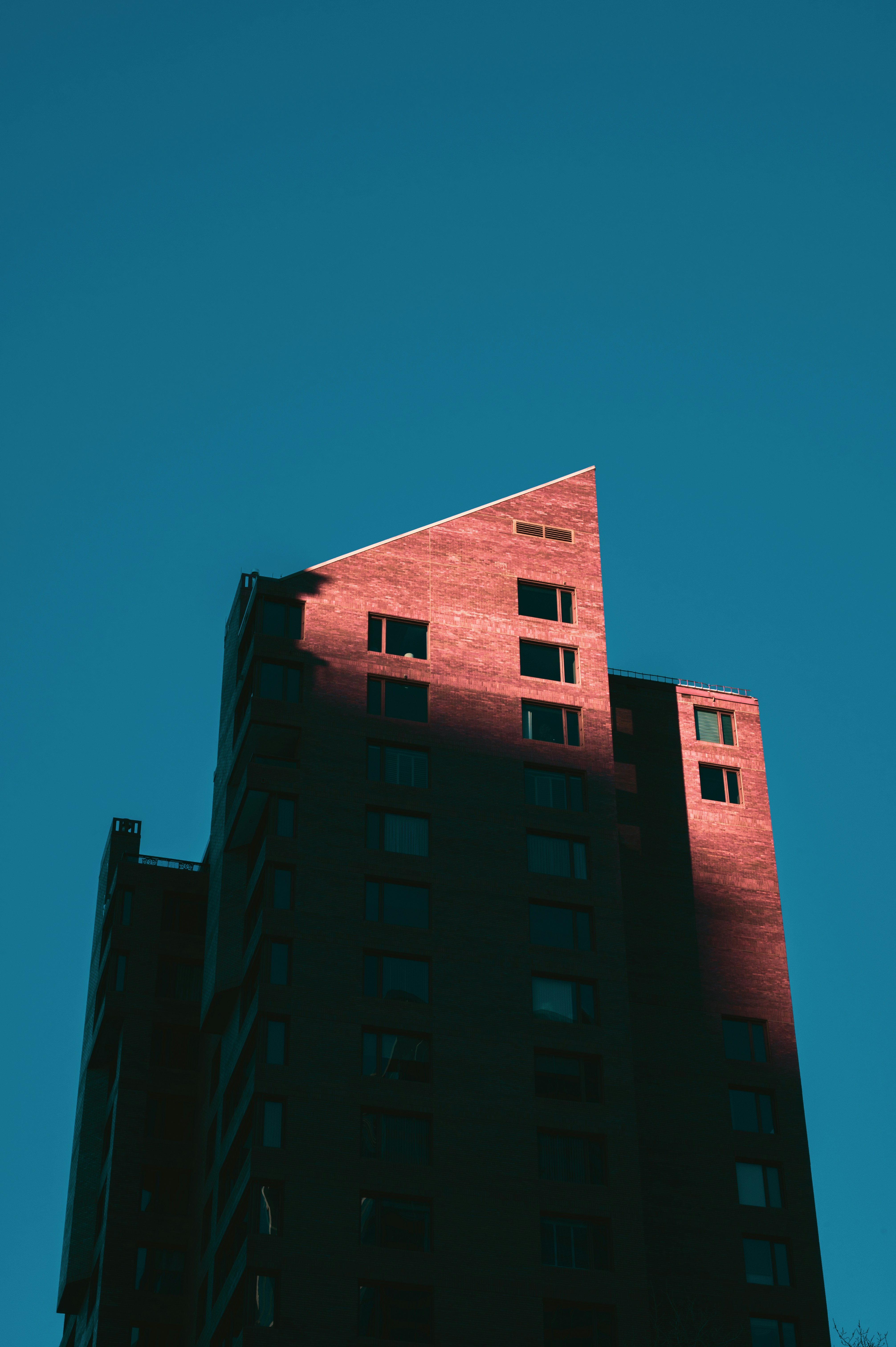 Angular brick building illuminated by sunlight against a clear blue sky, creating striking contrasts and shadows.