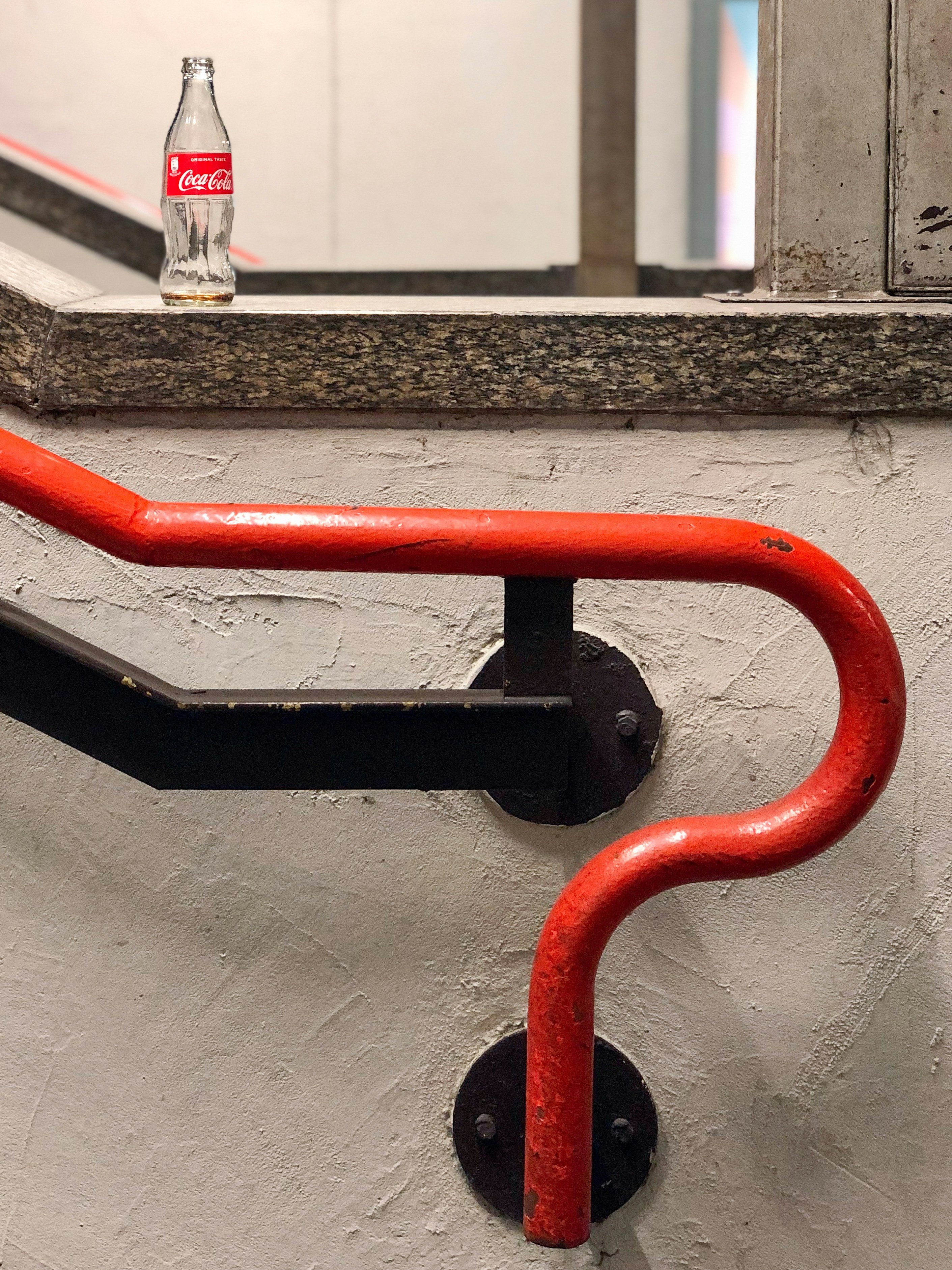 Coca-Cola on a Weathered Ledge Above a Crimson Handrail