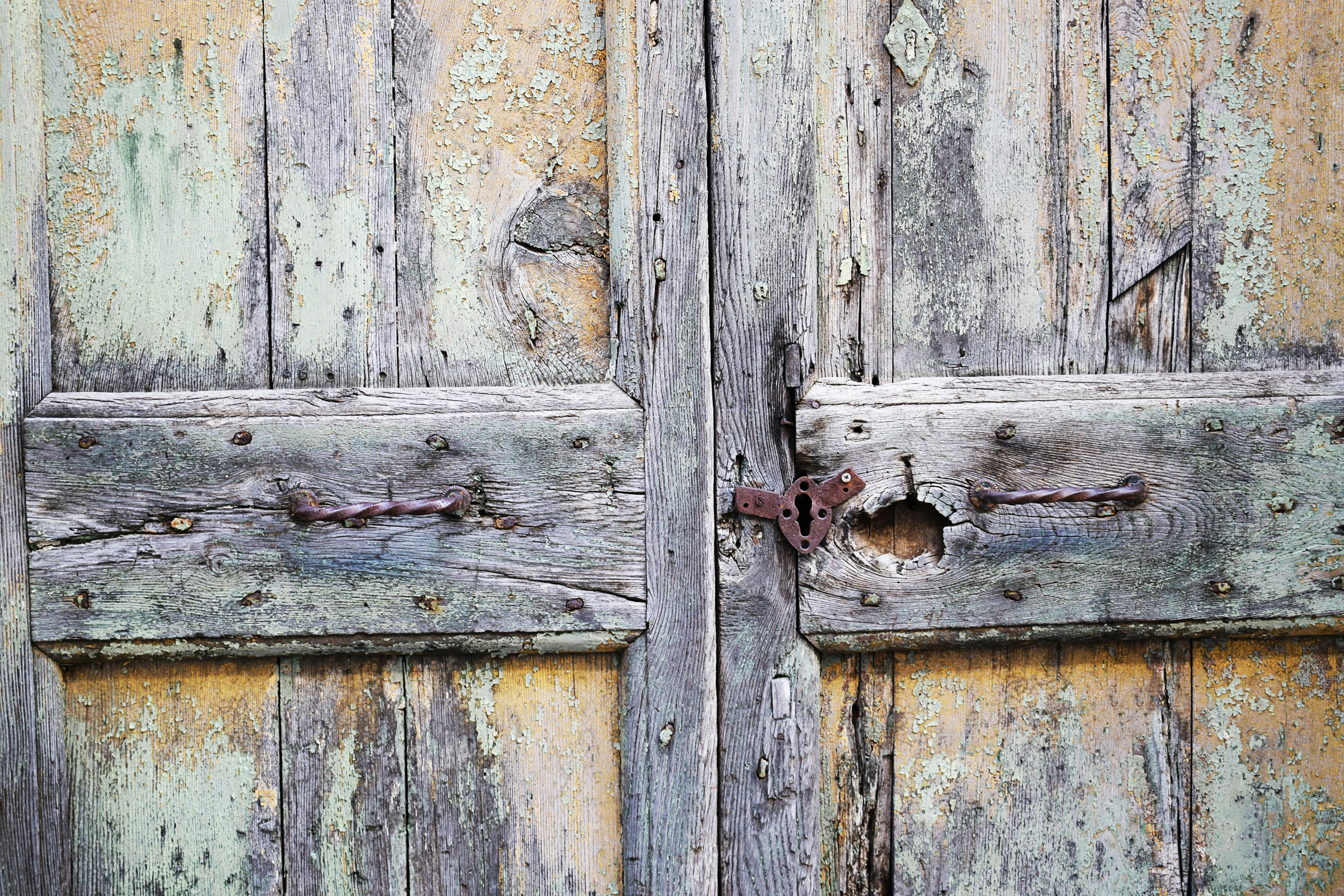 A weathered wooden door with peeling paint and rusted metal handles.