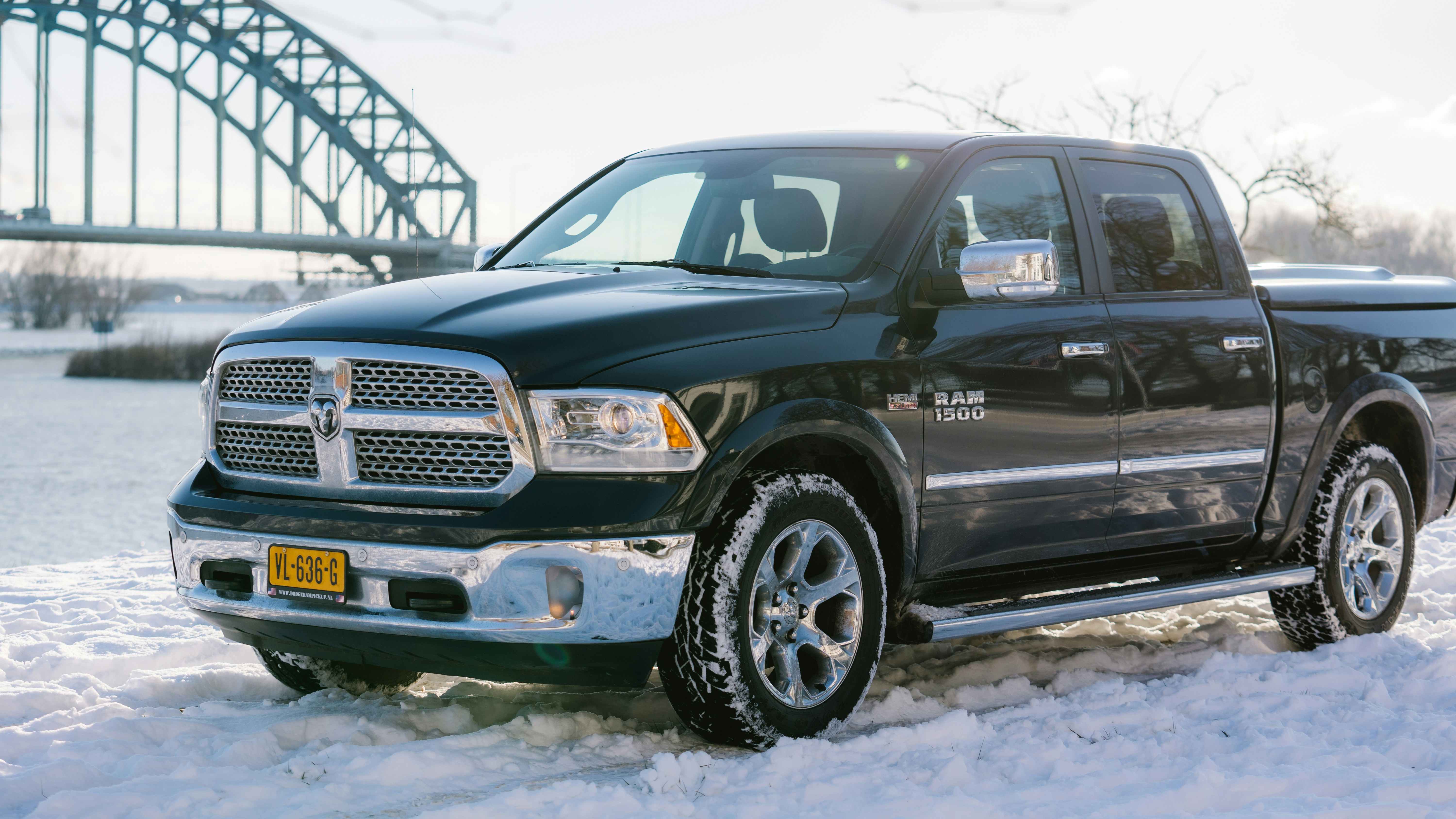 Black Dodge Ram pickup truck parked on snow-covered ground near an arched bridge.