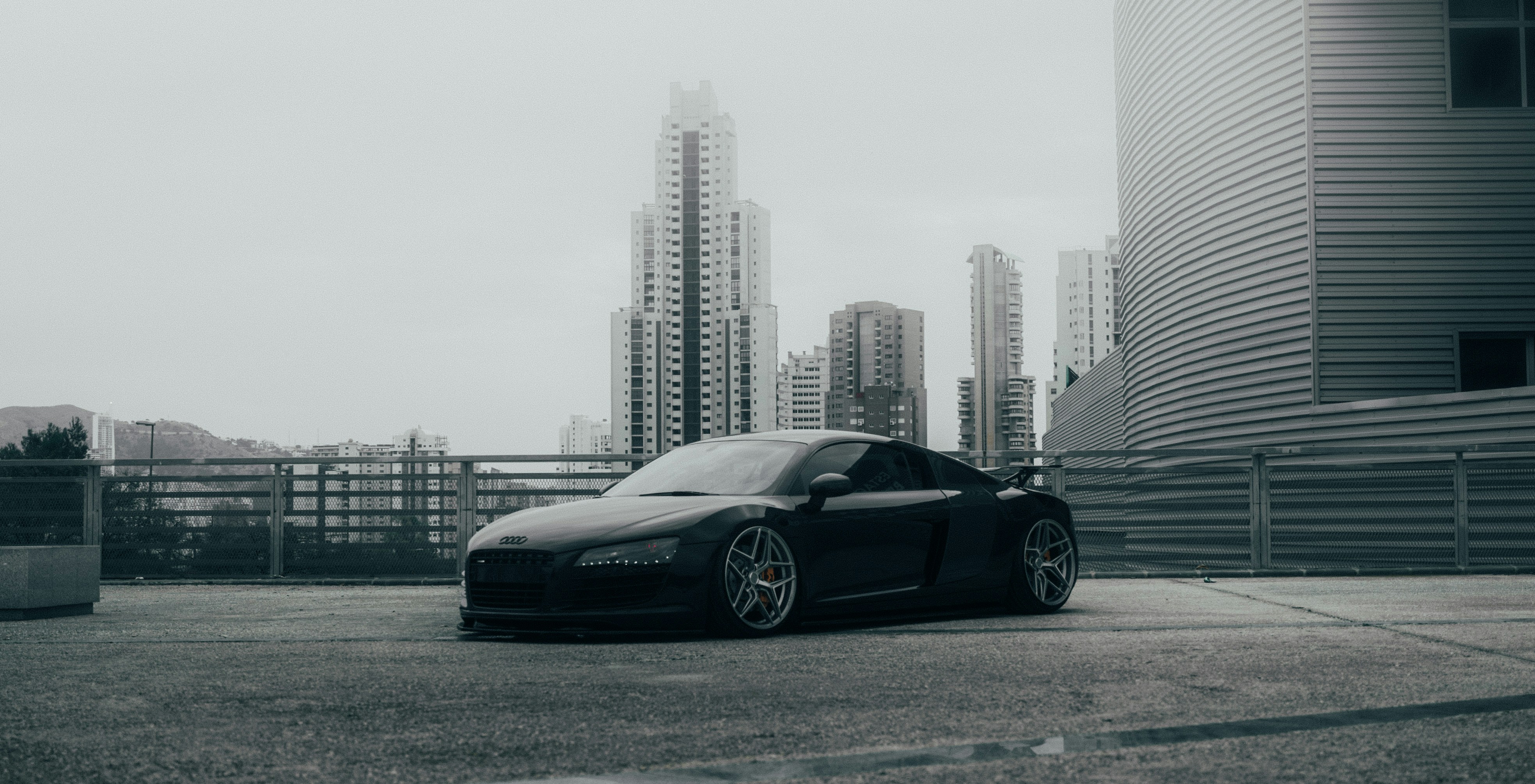 Sleek black sports car positioned against a backdrop of towering skyscrapers, showcasing a blend of modern architecture and automotive design.