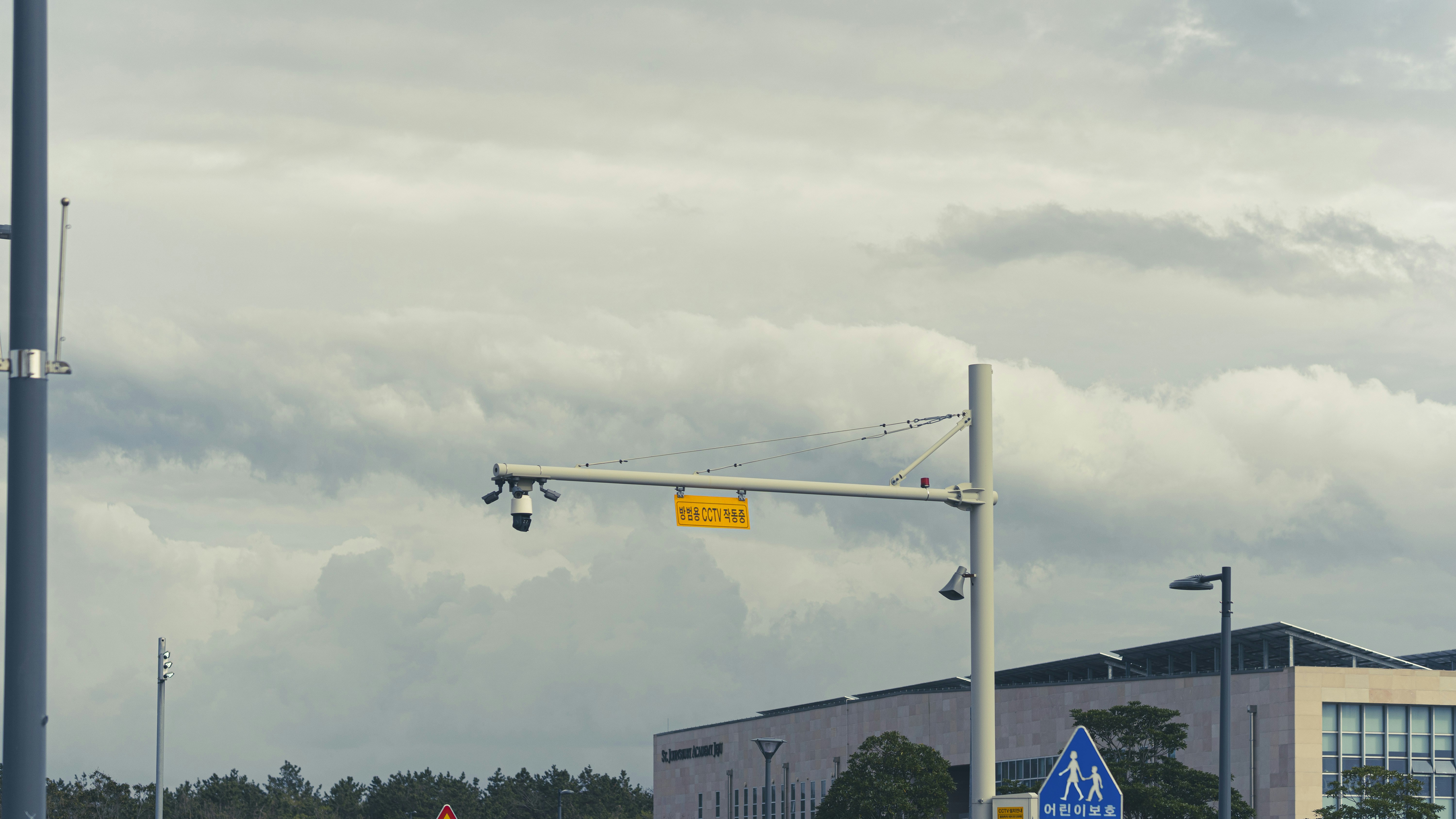 Traffic monitoring system with overhead cameras and signage against a backdrop of cloudy skies and modern architecture.