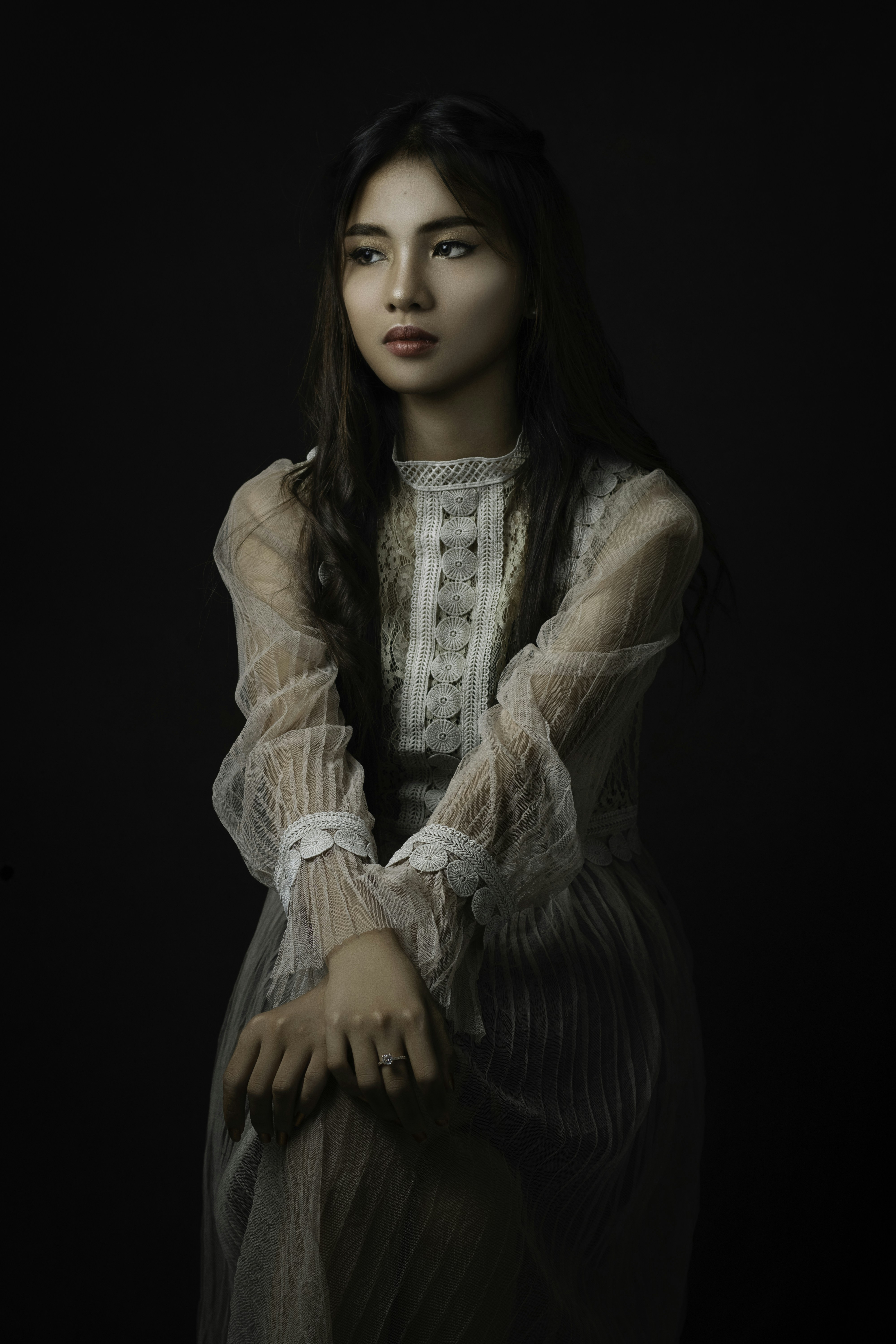 A serene portrait of a young woman in a delicate, sheer dress, set against a dark background, conveying a sense of introspection and grace.