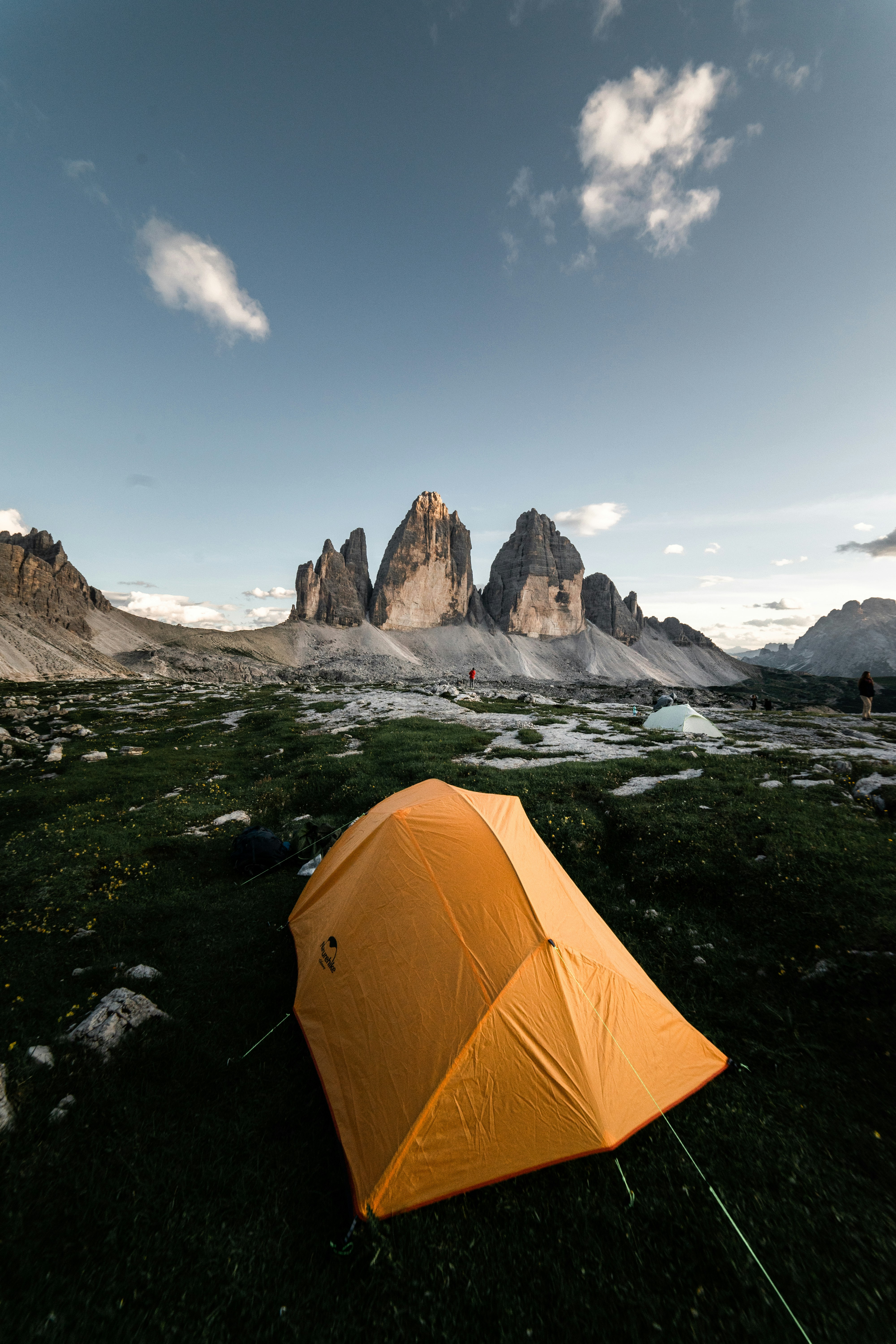 Brown tent on green grass field near gray rocky mountain under blue sky ...