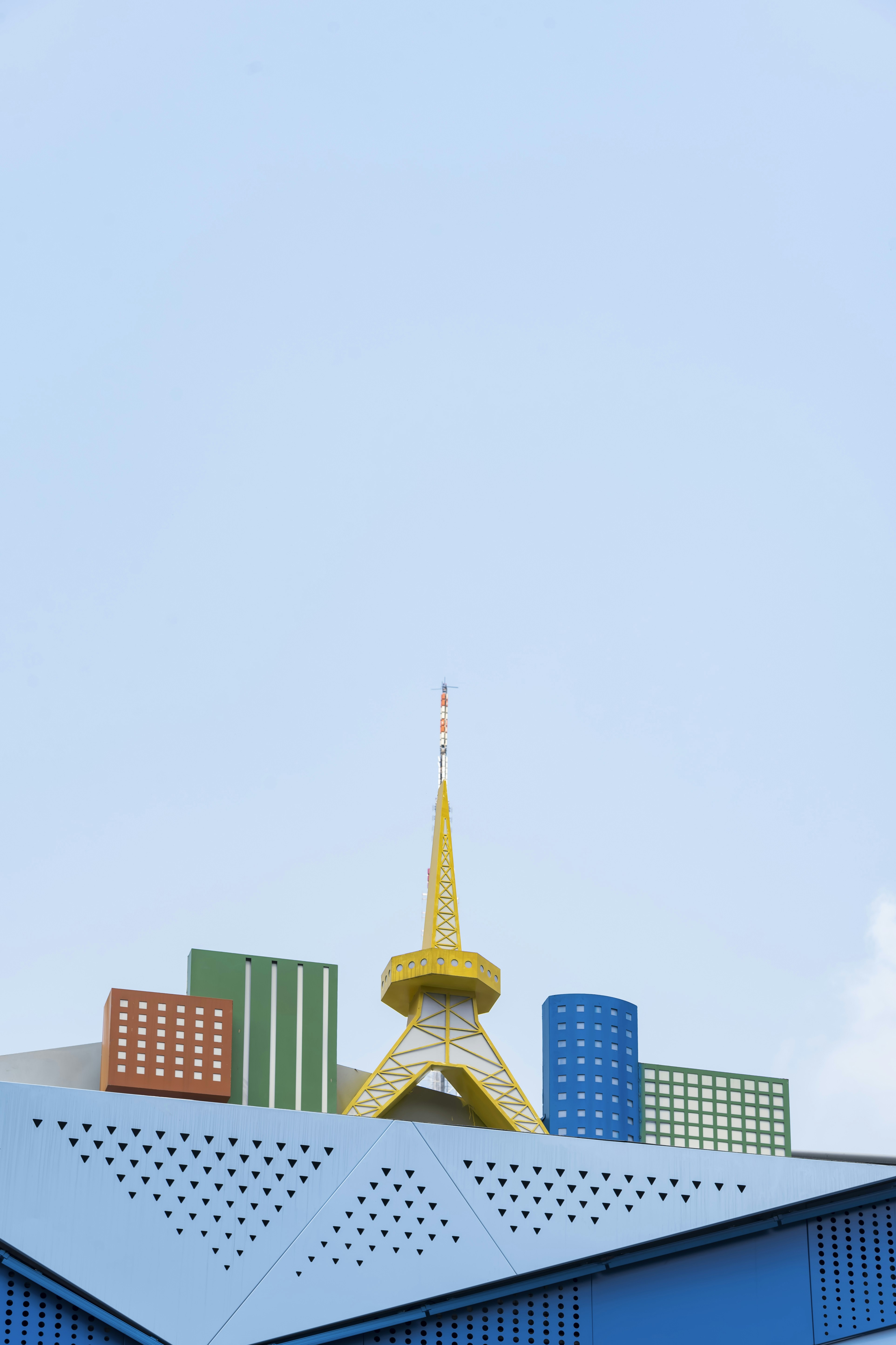 Colorful buildings with a yellow tower atop a blue structure against a clear sky. A whimsical representation of an urban landscape.