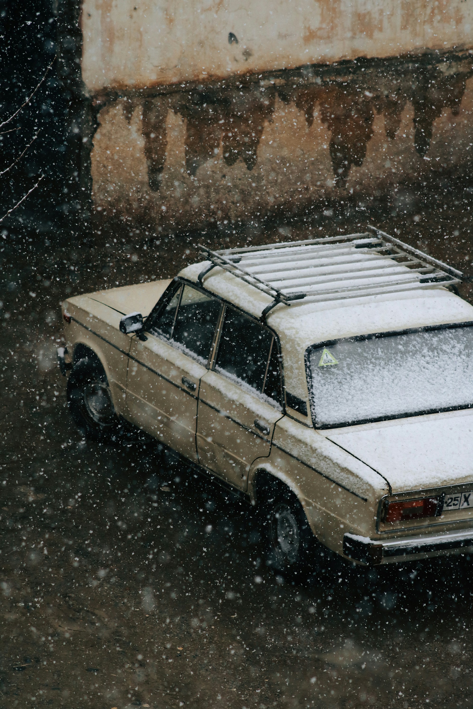 Winter Snowstorm Encases a Beige Vintage Sedan by a Weathered Wall