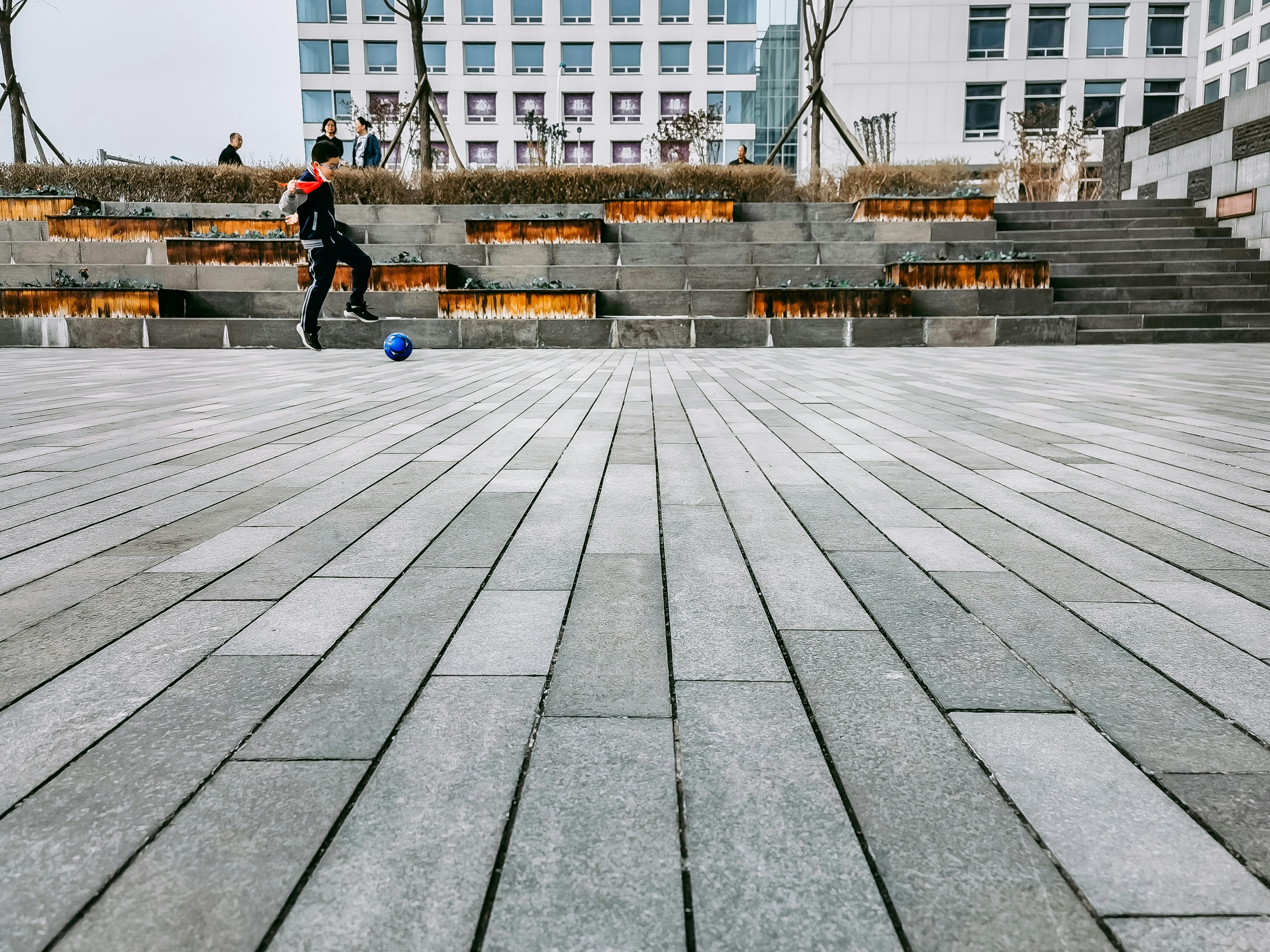 Urban Staircase Sprint: A Lone Runner Dribbles a Cobalt Ball Across a Modern Plaza