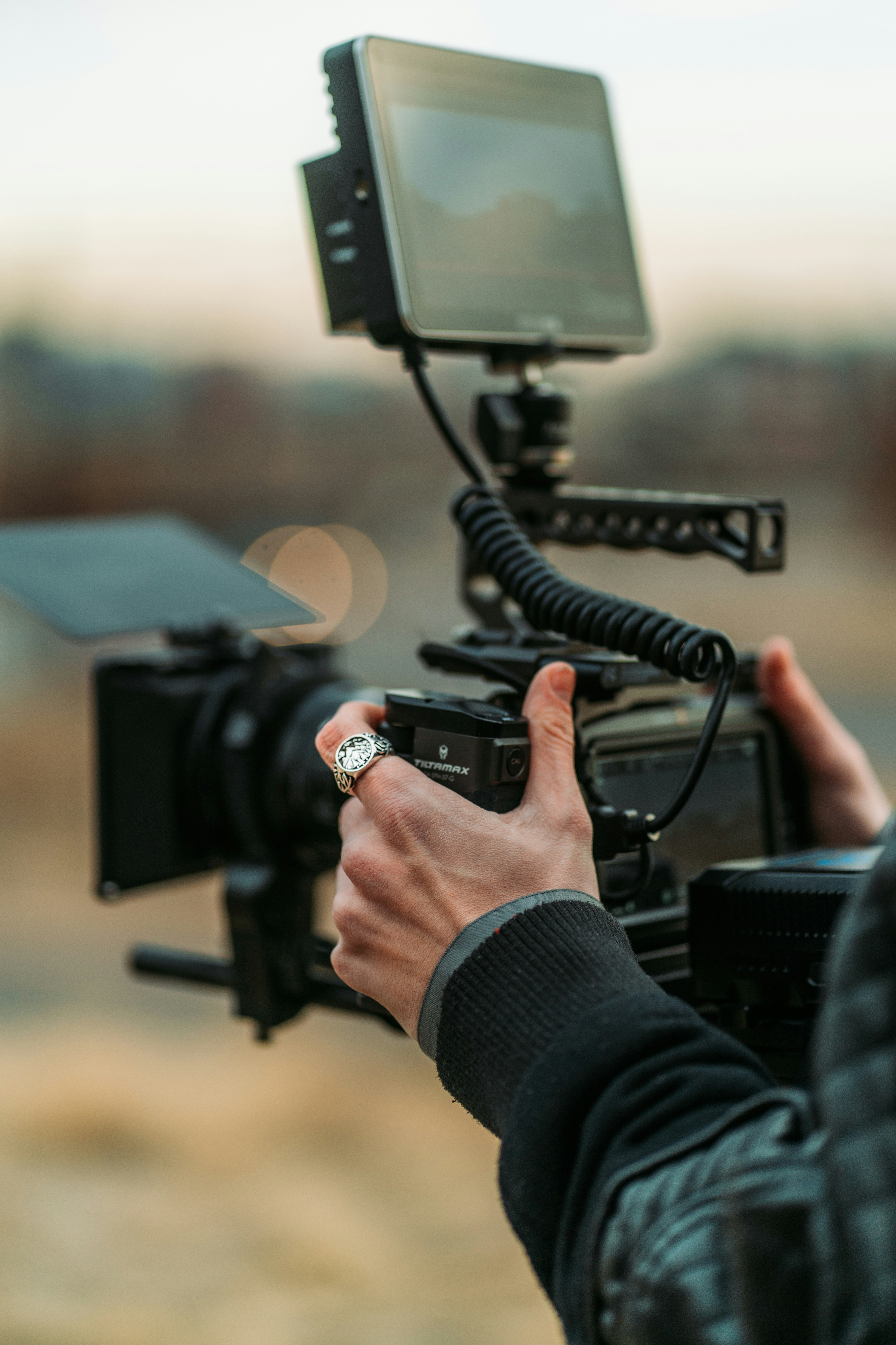A filmmaker grips a camera rig, showcasing the intricate setup for capturing cinematic footage. The scene is set against a blurred background, hinting at a creative process in action.