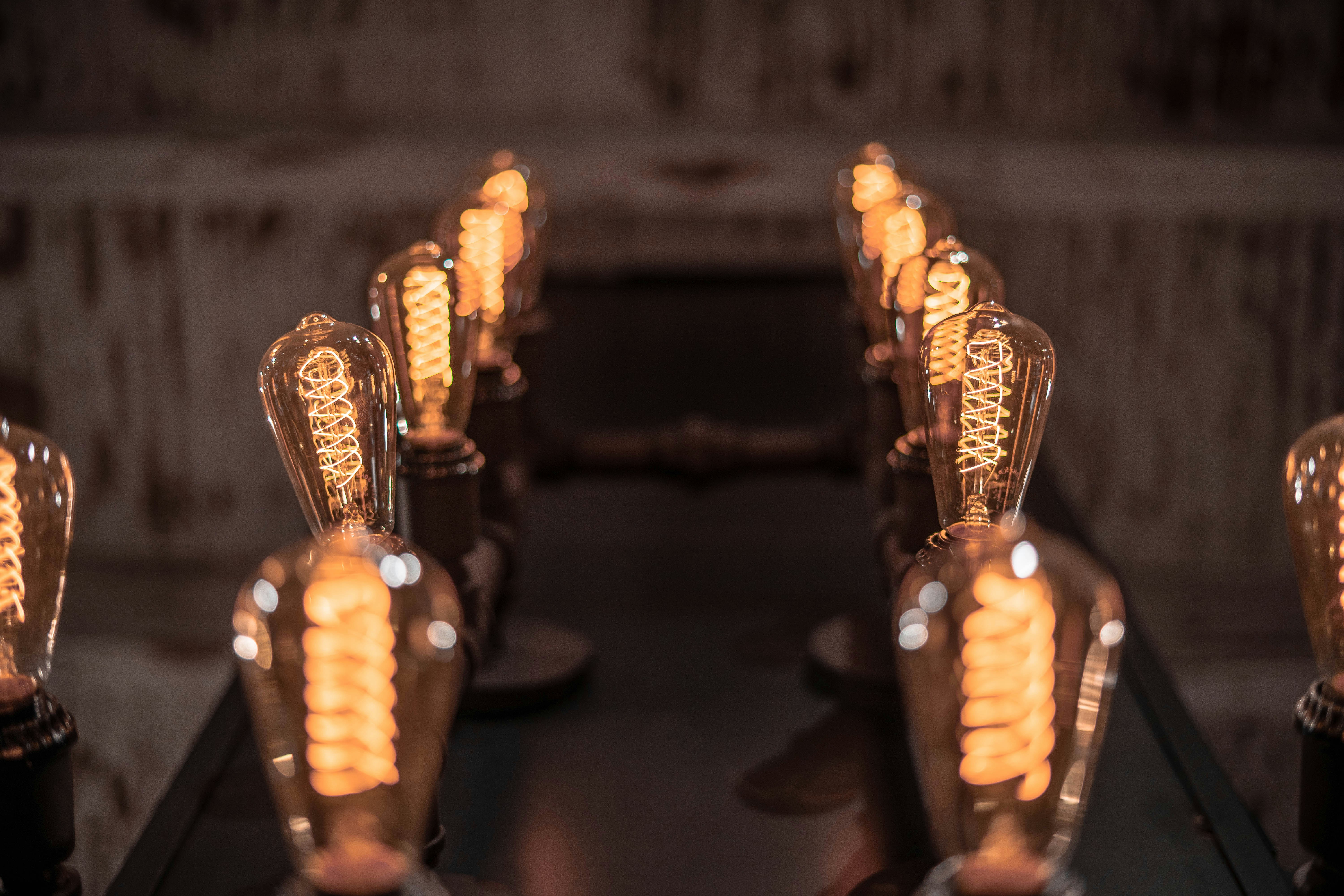 A row of vintage light bulbs emitting a warm glow, showcasing intricate filament designs against a rustic backdrop.