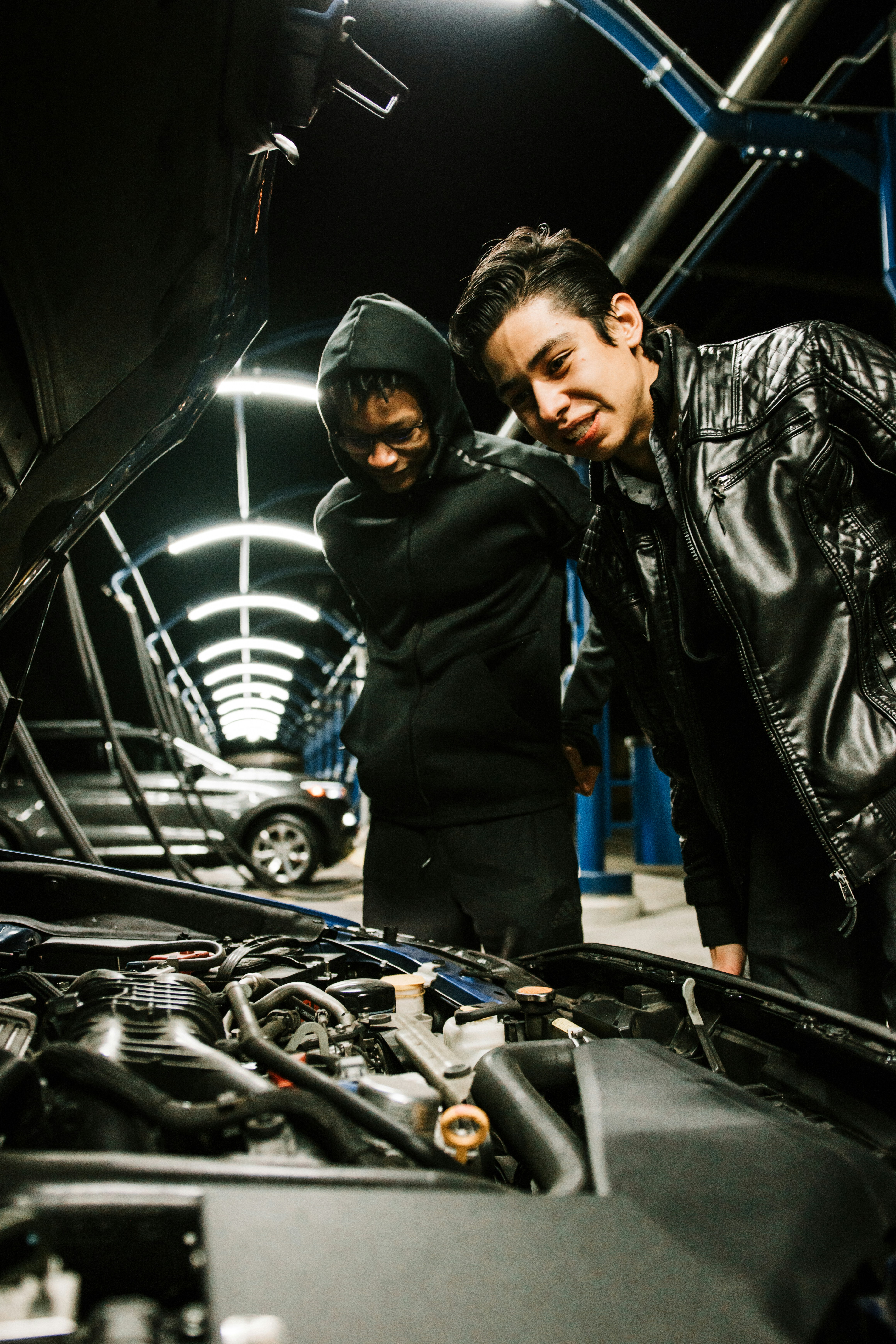 Under the Hood: Two Friends Inspect a Car in a Neon-lit Tunnel