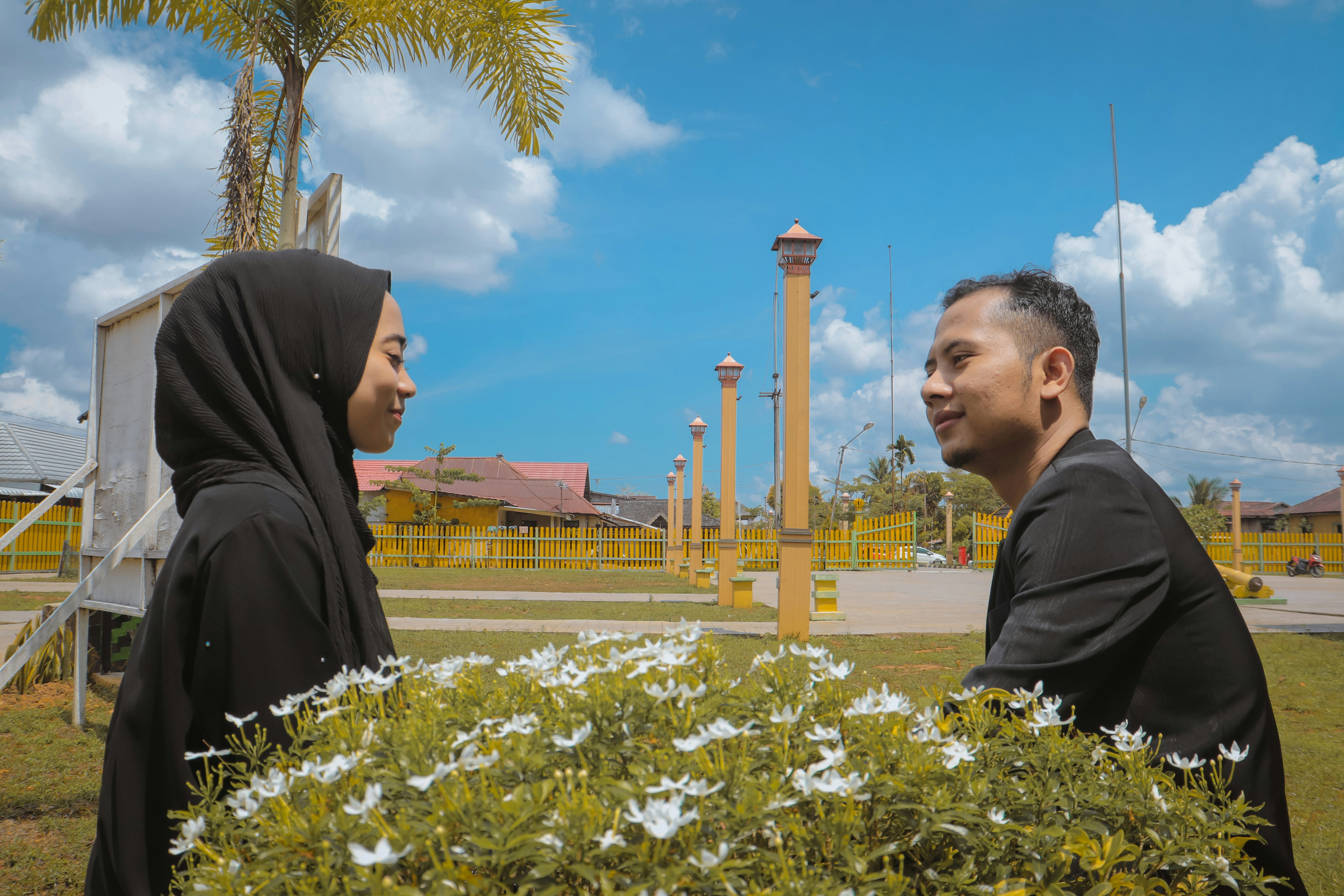 Two individuals engaged in a heartfelt conversation, framed by vibrant flowers and a clear blue sky.