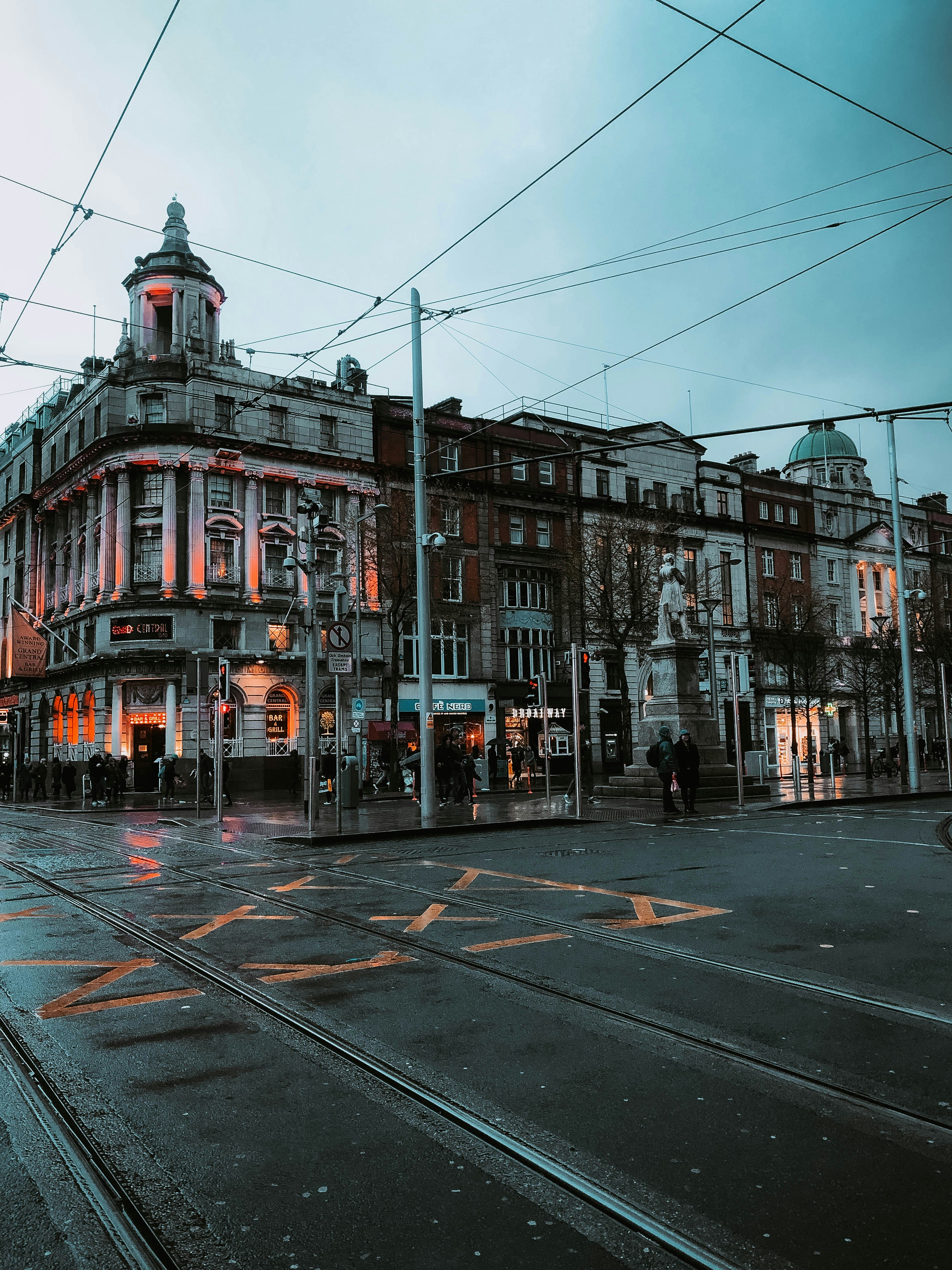 Historic building illuminated by warm lights amidst a rainy urban landscape, with reflections on wet pavement. A blend of modern and classic architecture.