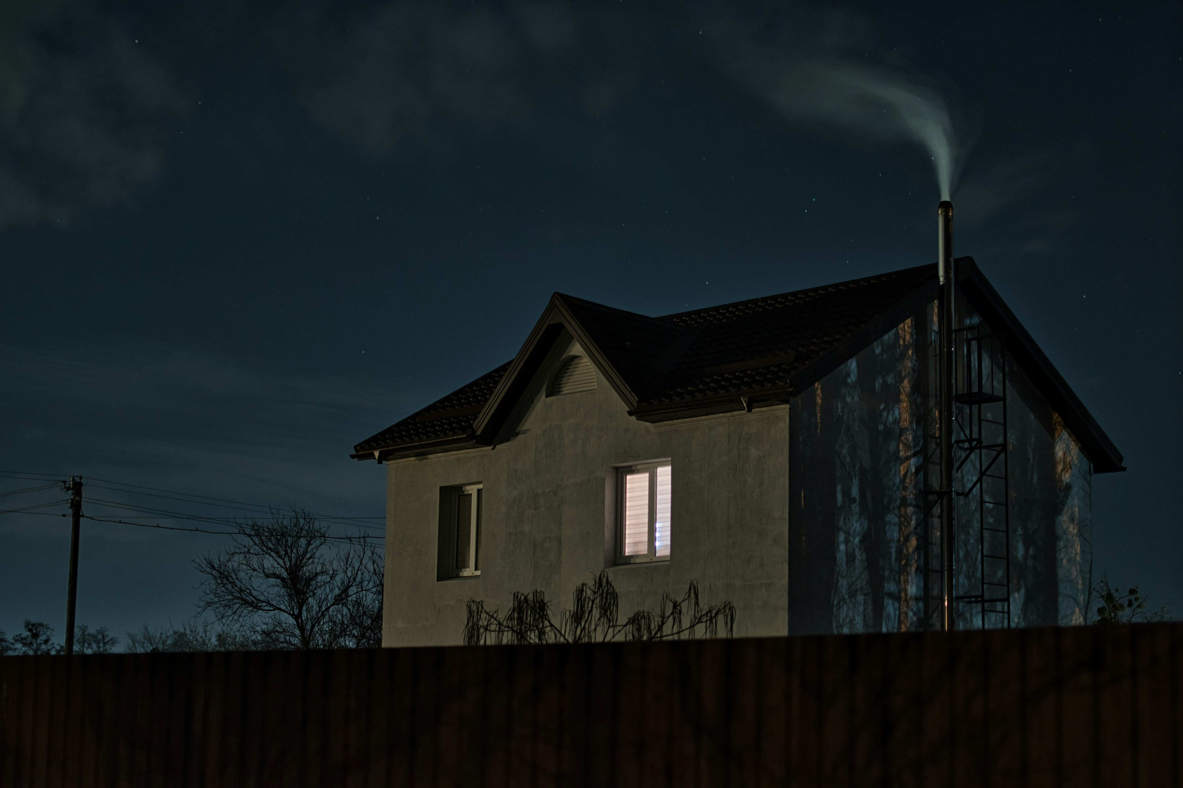 A solitary house under a starry sky, with smoke drifting from its chimney and a warm glow emanating from the window.