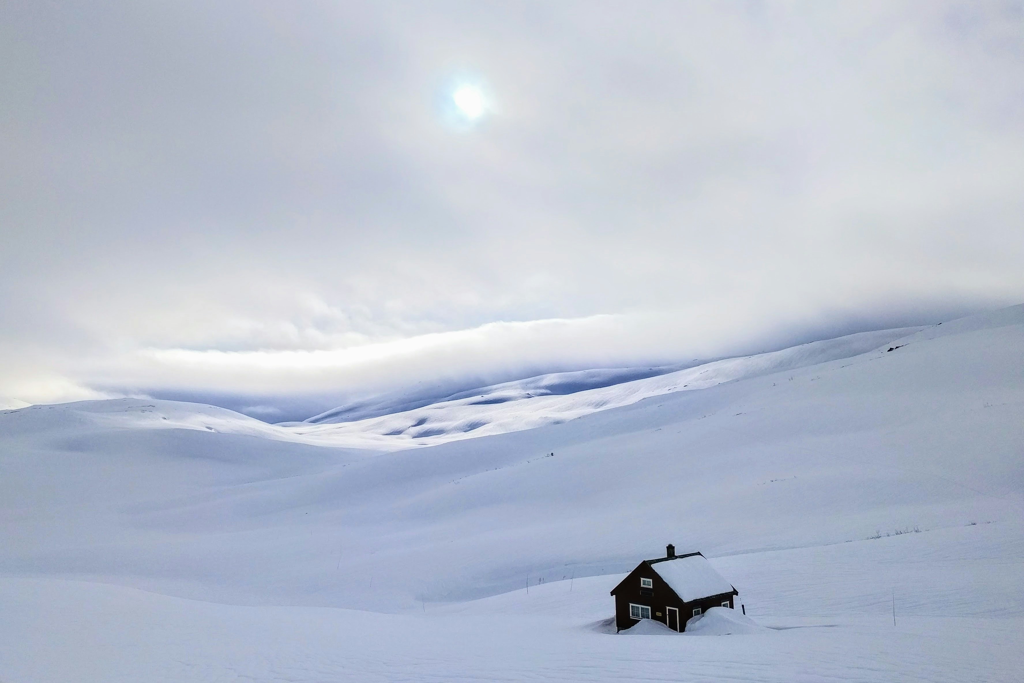 A quaint cabin nestled in a vast snowy landscape under a cloudy sky. The scene conveys a sense of tranquility and isolation.