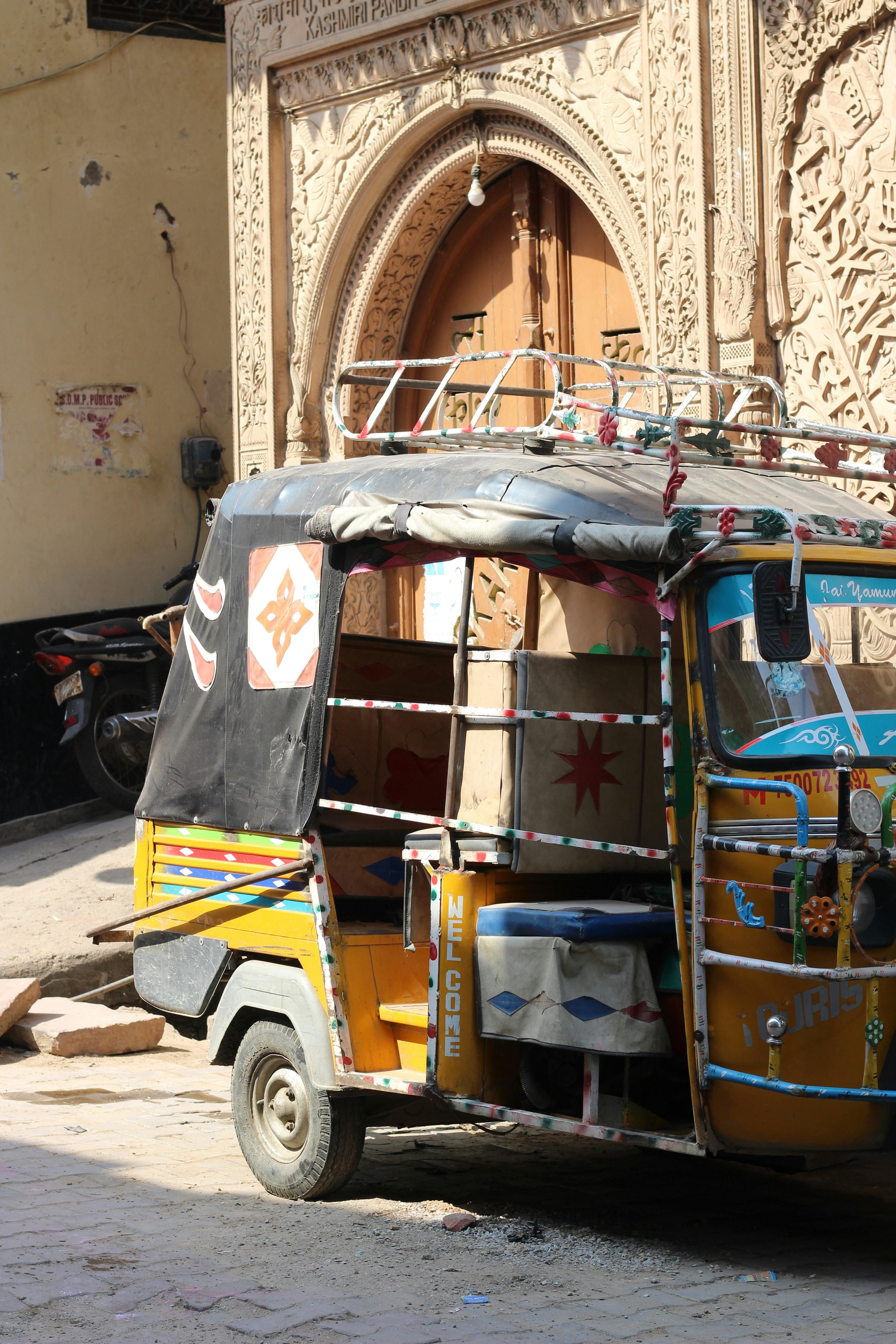Colorful auto-rickshaw parked beside intricately carved historical architecture in a bustling street.
