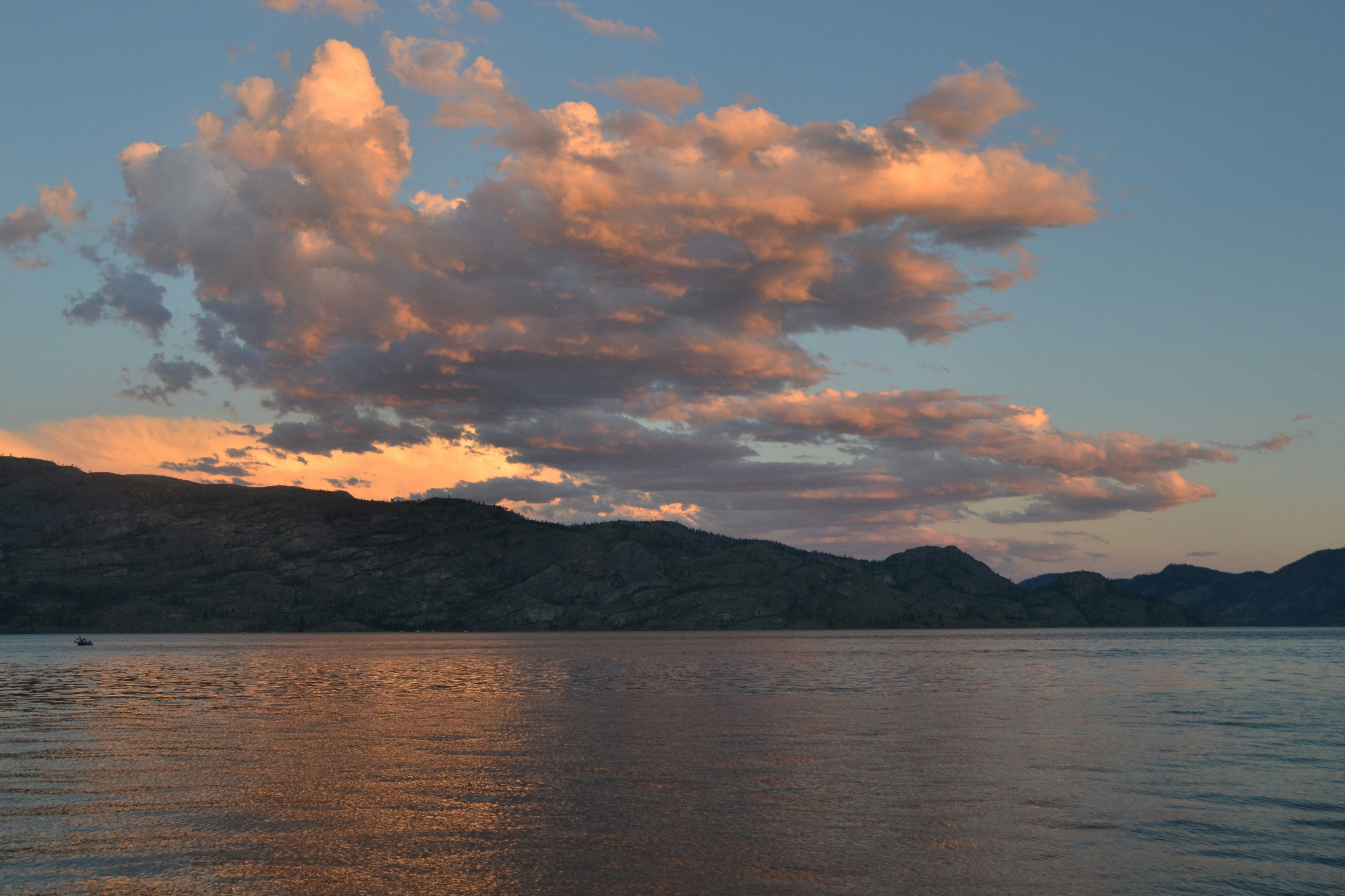 Soft clouds reflecting warm hues above a serene lake, framed by distant mountains at dusk.