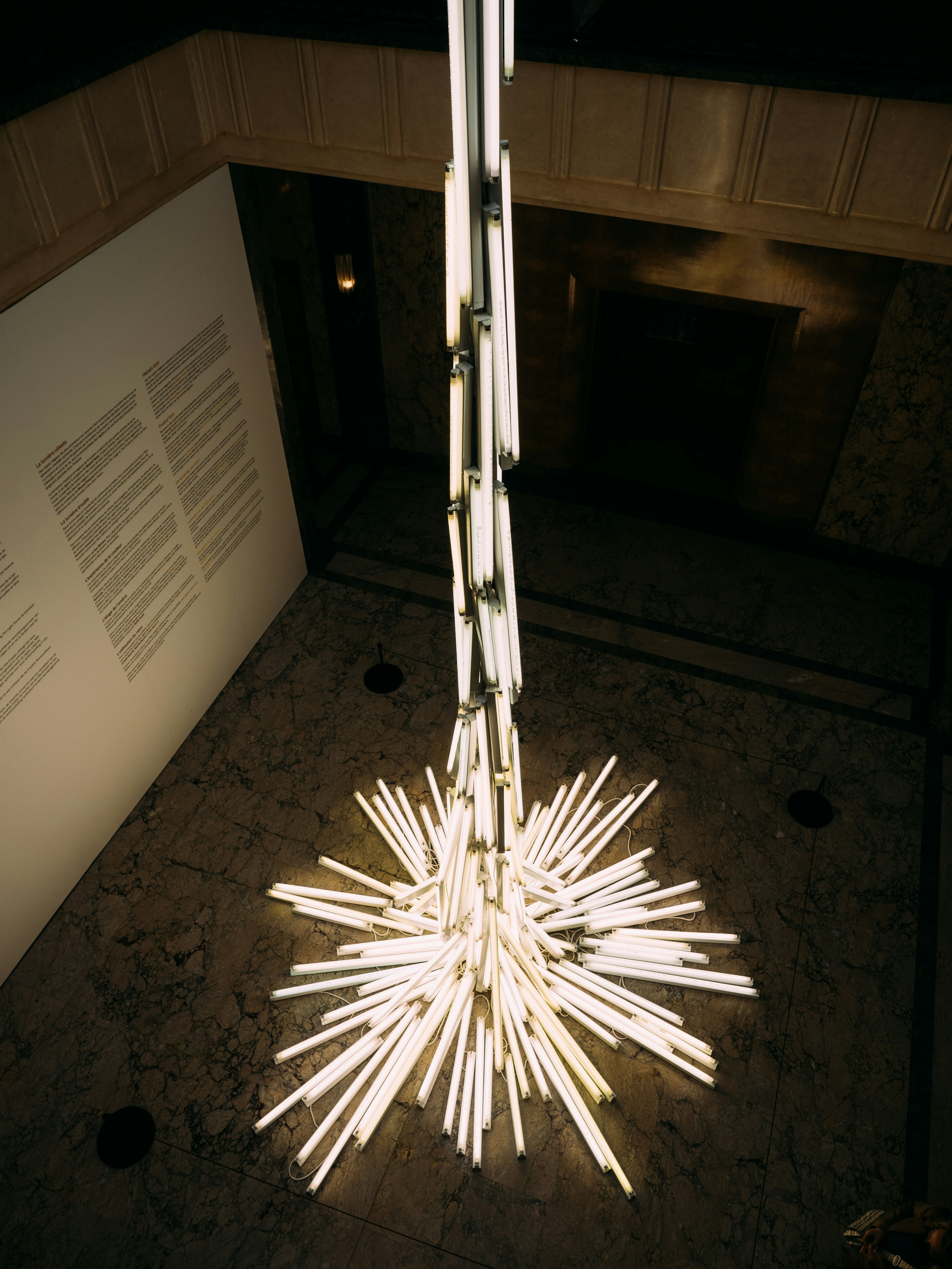 Unique chandelier composed of illuminated tubes, radiating from a central point in a modern architectural space.