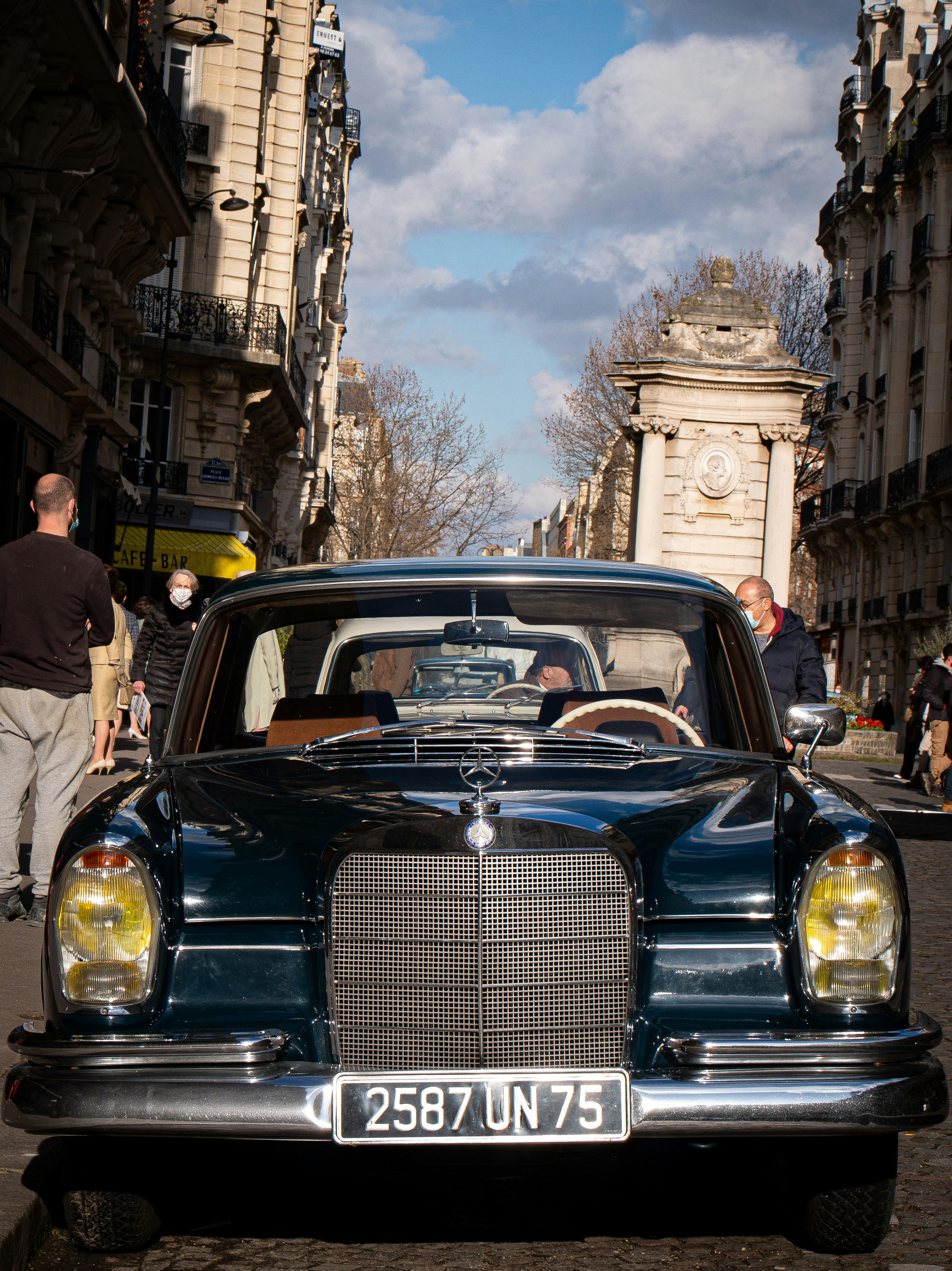 Classic vintage car parked on a cobblestone street, framed by historic buildings and a clear blue sky. The scene captures the essence of Parisian charm.
