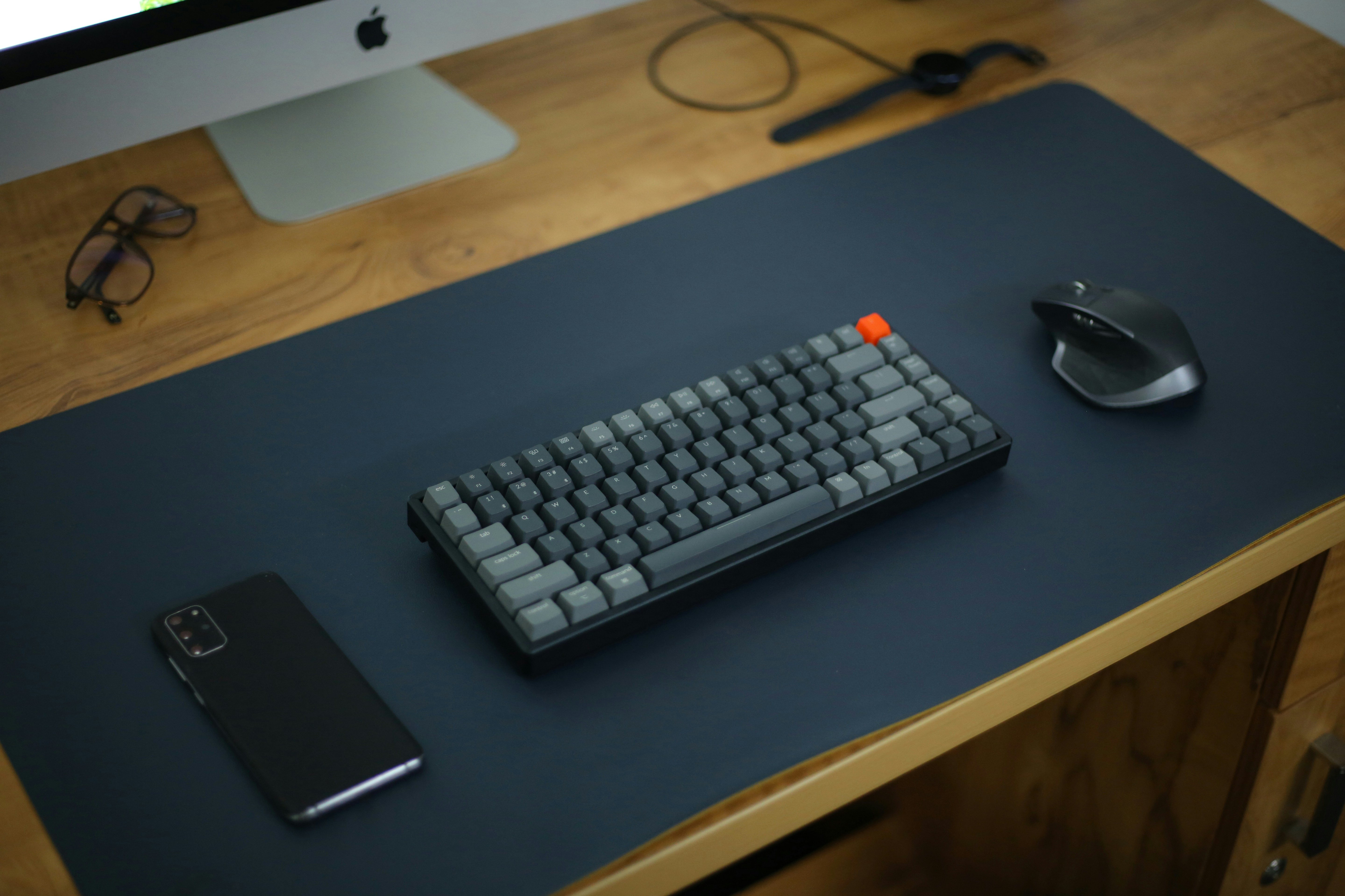 A sleek mechanical keyboard, an ergonomic mouse, and a smartphone arranged neatly on a stylish desk mat, showcasing a contemporary workspace aesthetic.