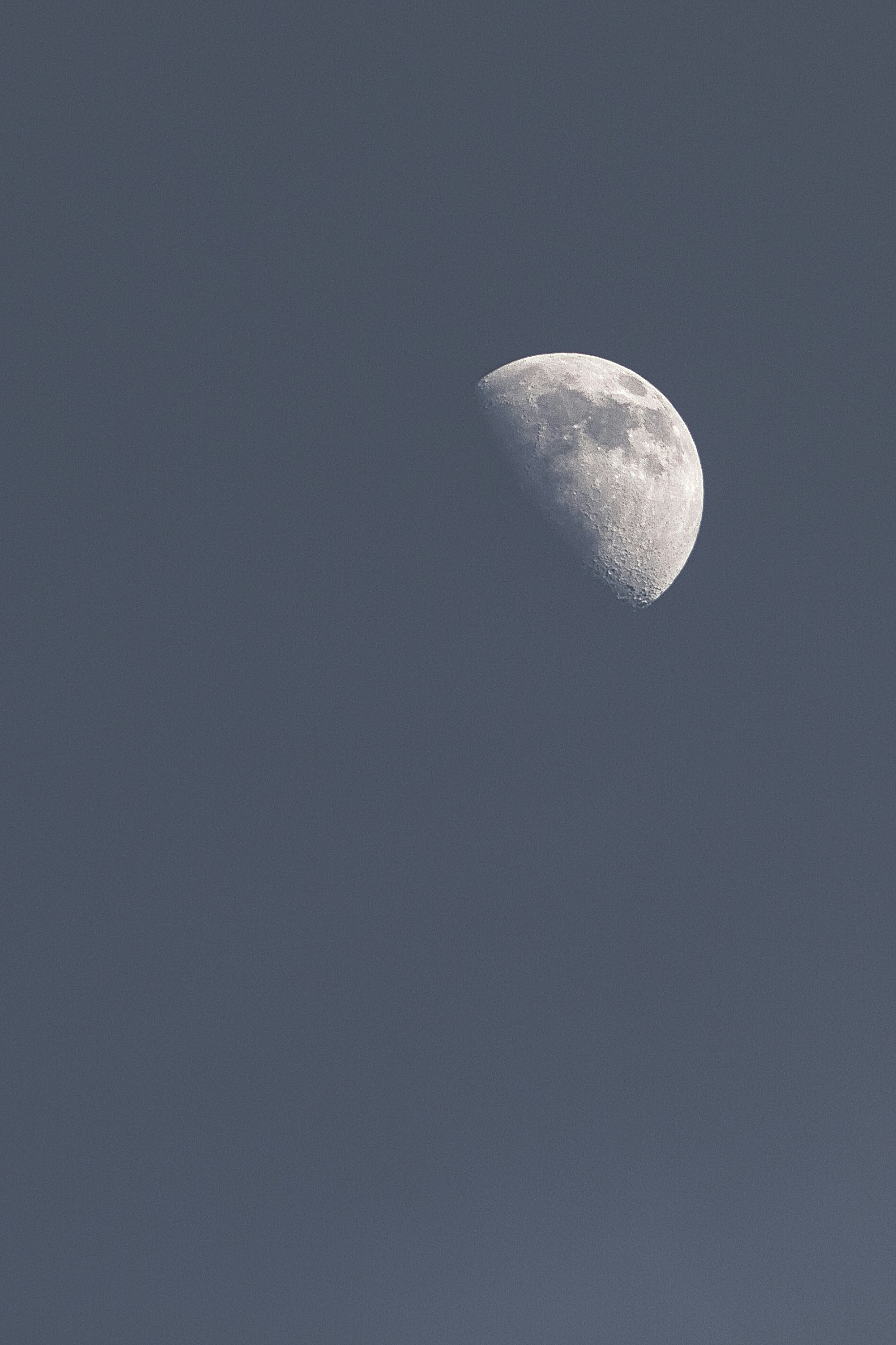 Crescent moon softly illuminated against a muted sky, showcasing its craters and textures.