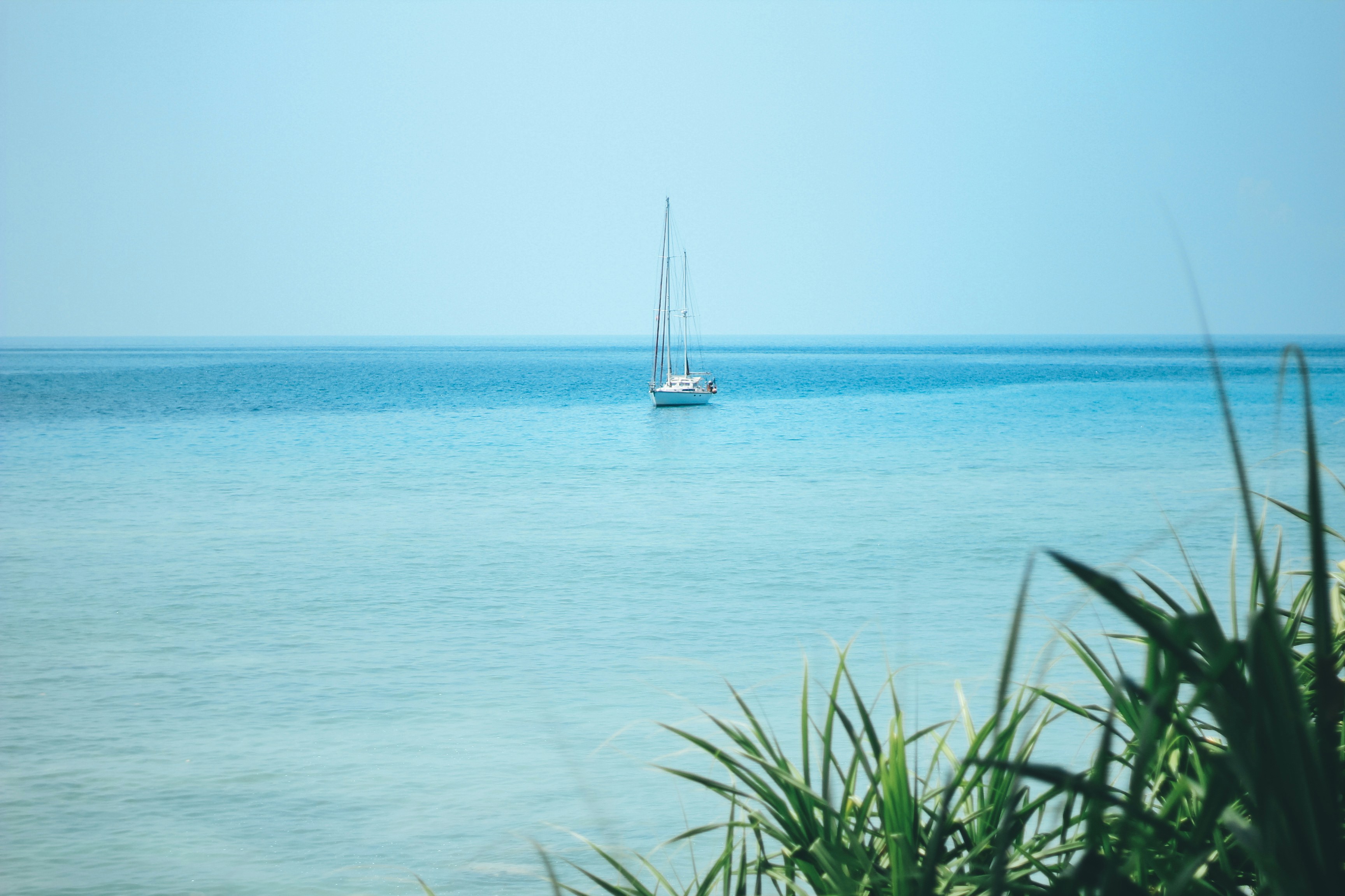 A sailboat gently floats on tranquil turquoise waters, framed by lush greenery at the shore. The scene evokes a sense of peace and relaxation.