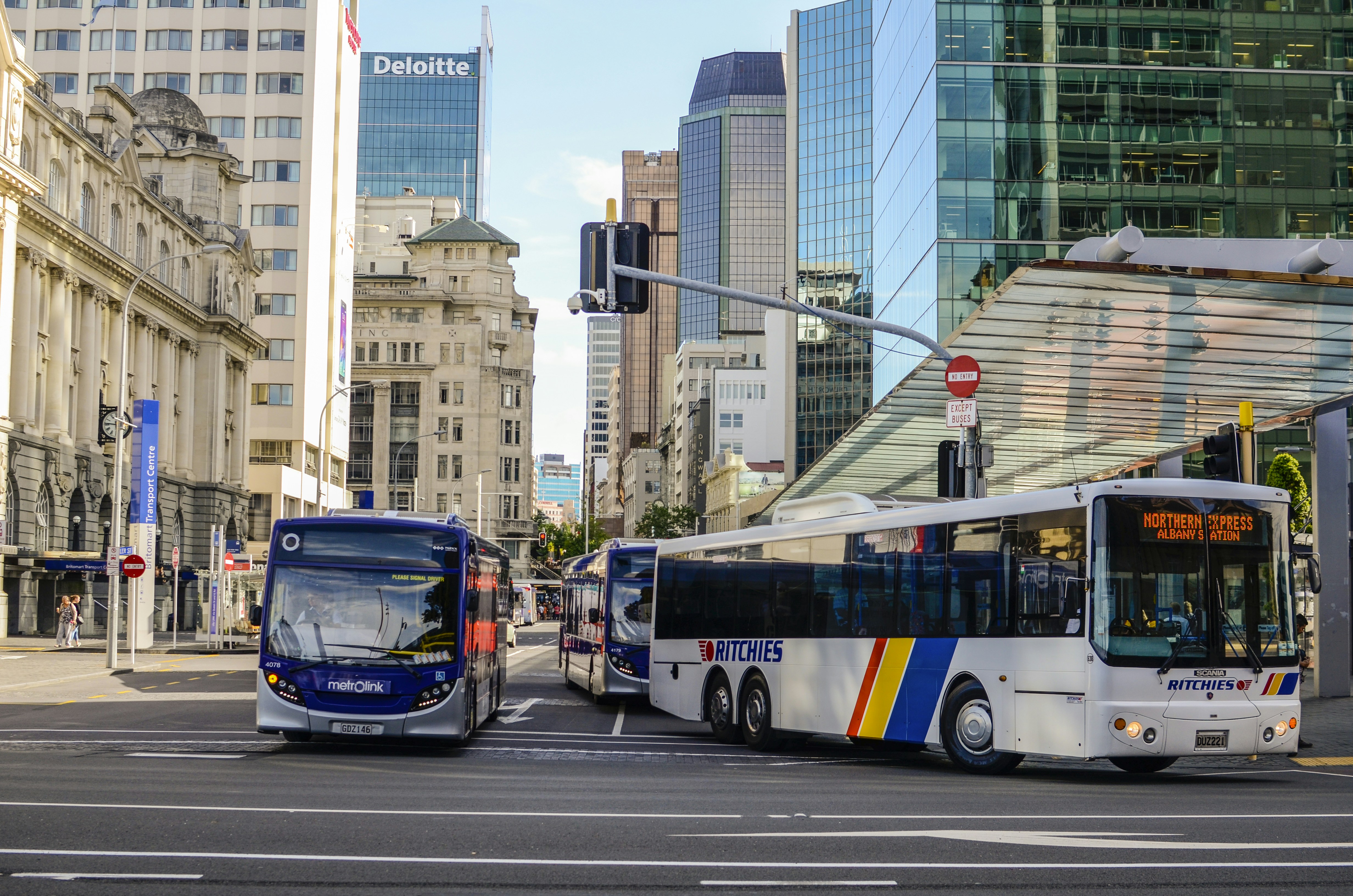 Buses navigate a bustling city intersection surrounded by modern skyscrapers and historic buildings.