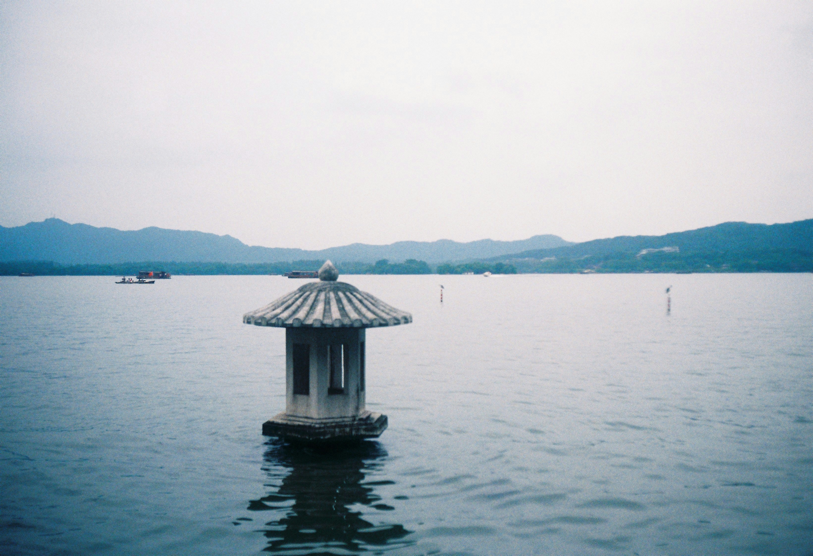 Stone lantern partially submerged in a tranquil lake with distant hills under a soft sky.