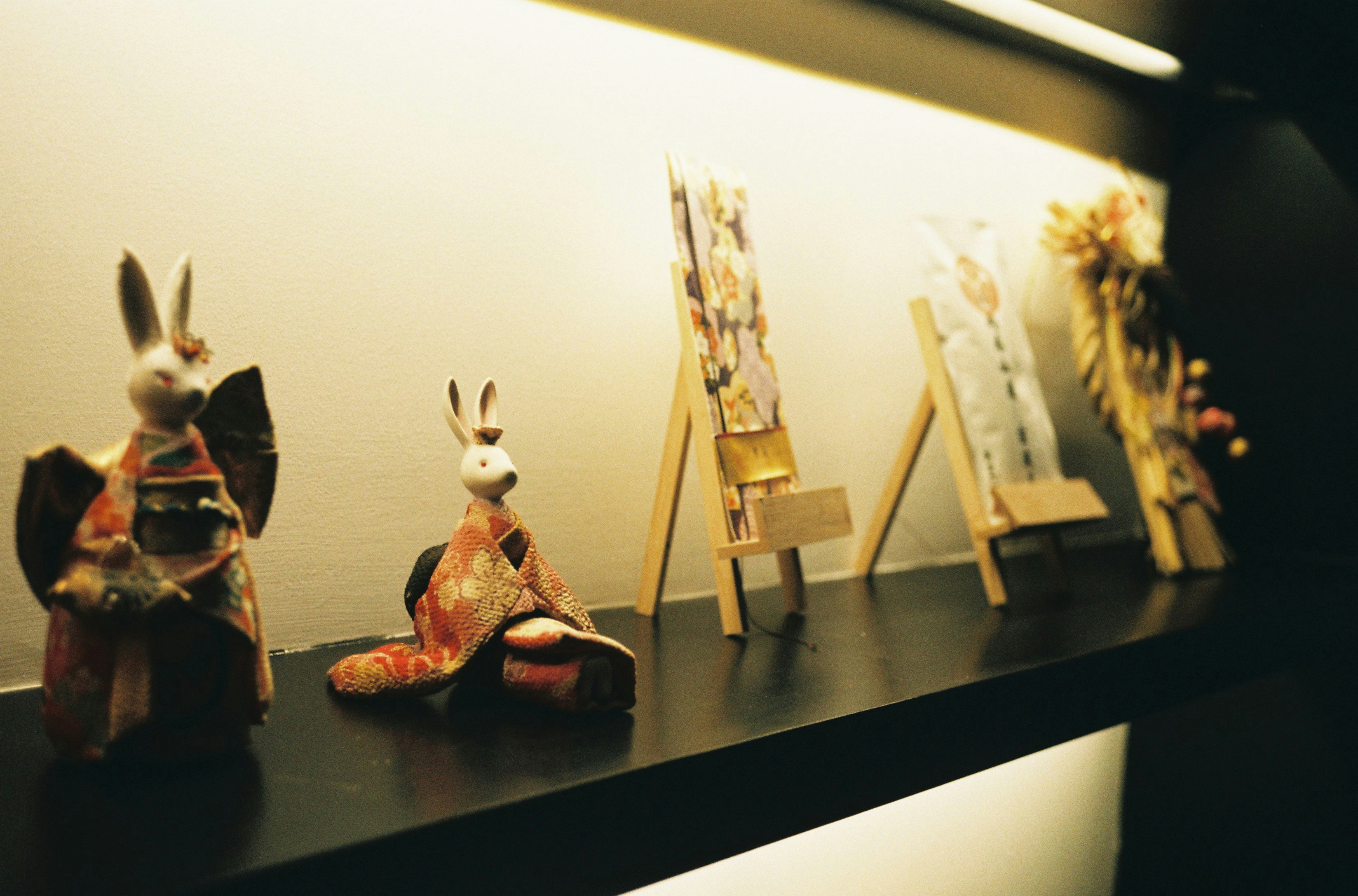 Decorative rabbit figurines dressed in traditional attire displayed on a dimly lit shelf.
