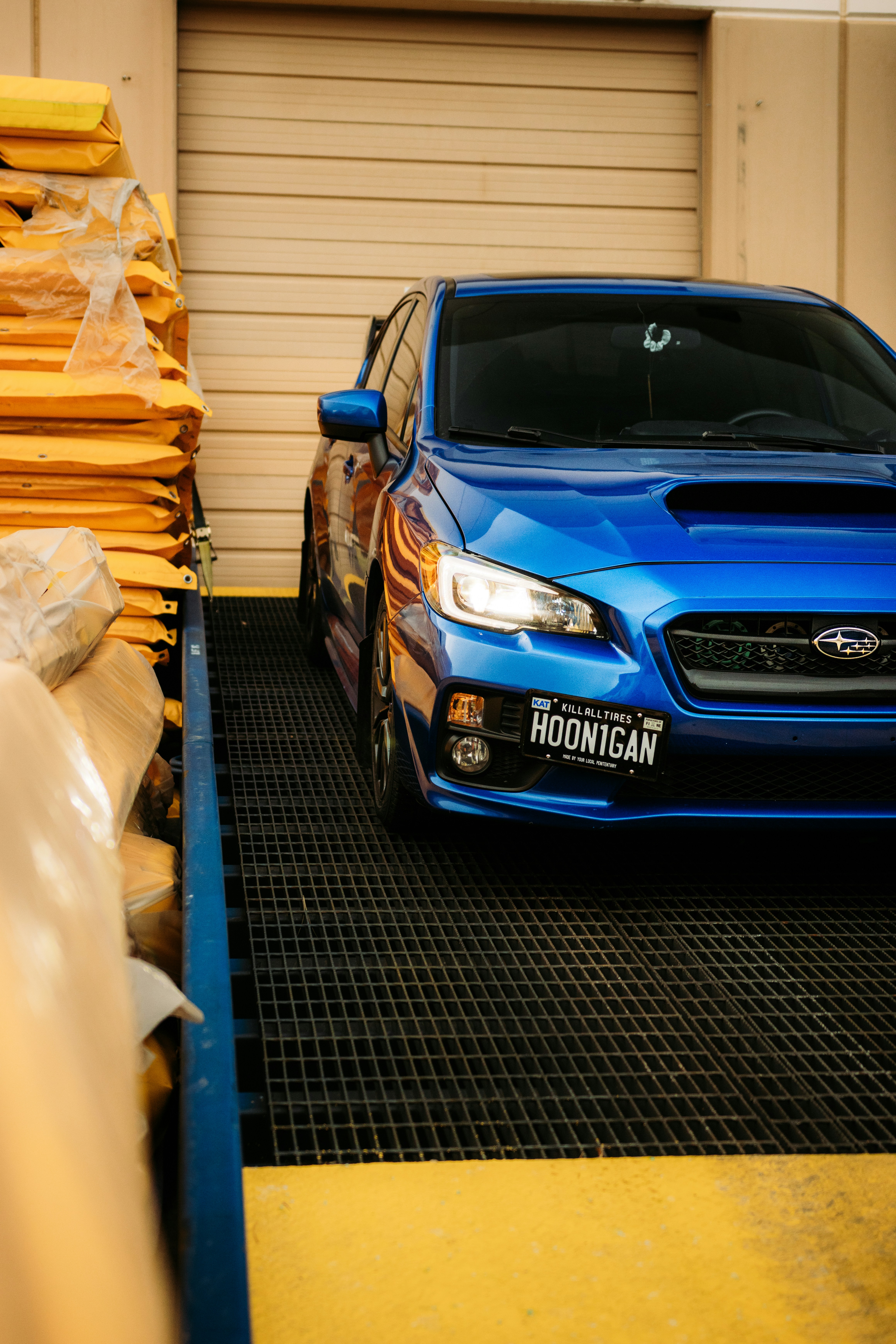 Blue Subaru at the Dock: Grille Spotlight Against Stacked Amber Pallets